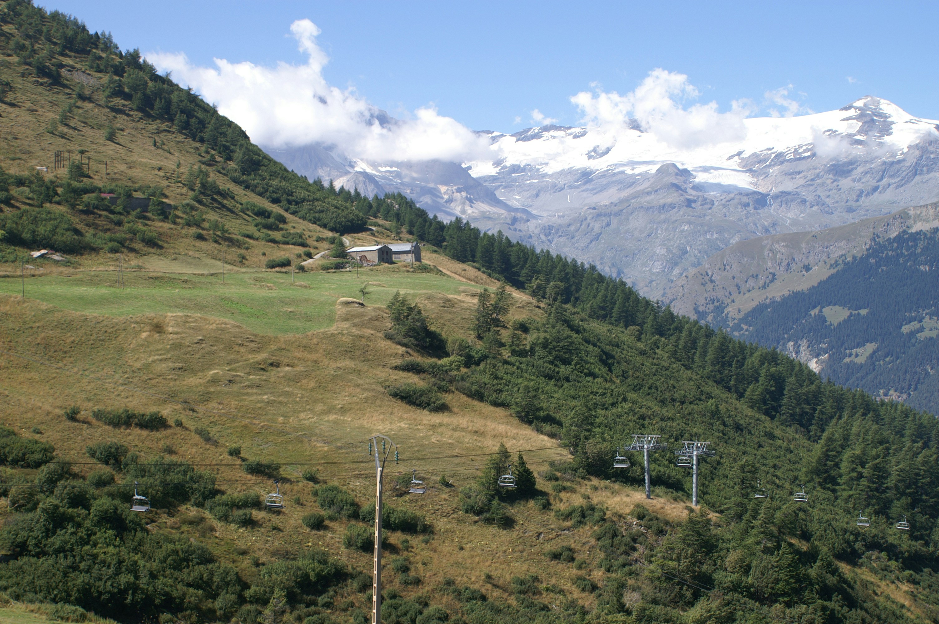 A serene mountain scene featuring a rustic cabin amidst rolling hills, with ski lifts in the foreground and majestic snow-capped peaks in the background.