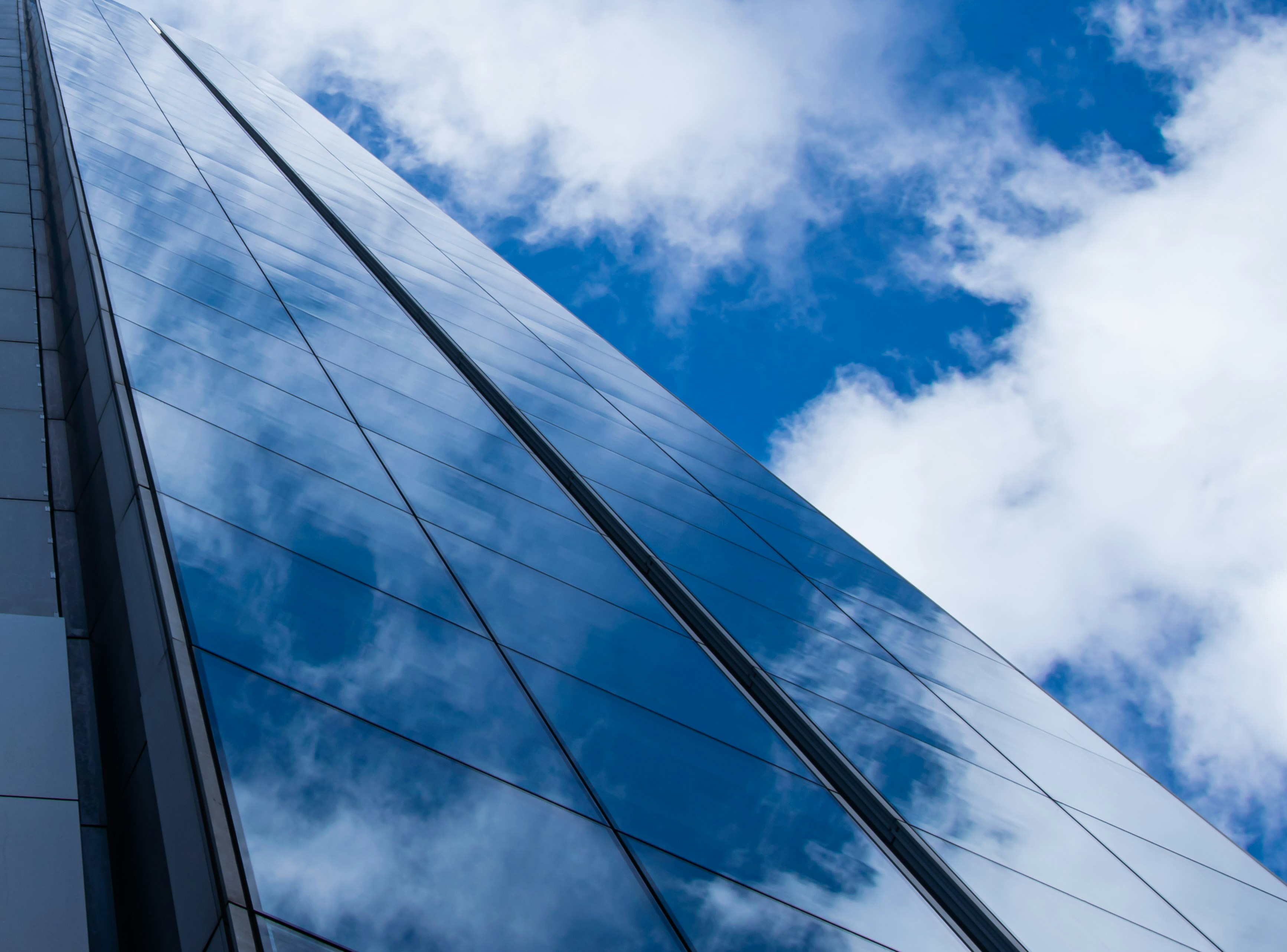 Tall glass building reflecting clouds and blue sky, showcasing modern architectural design.