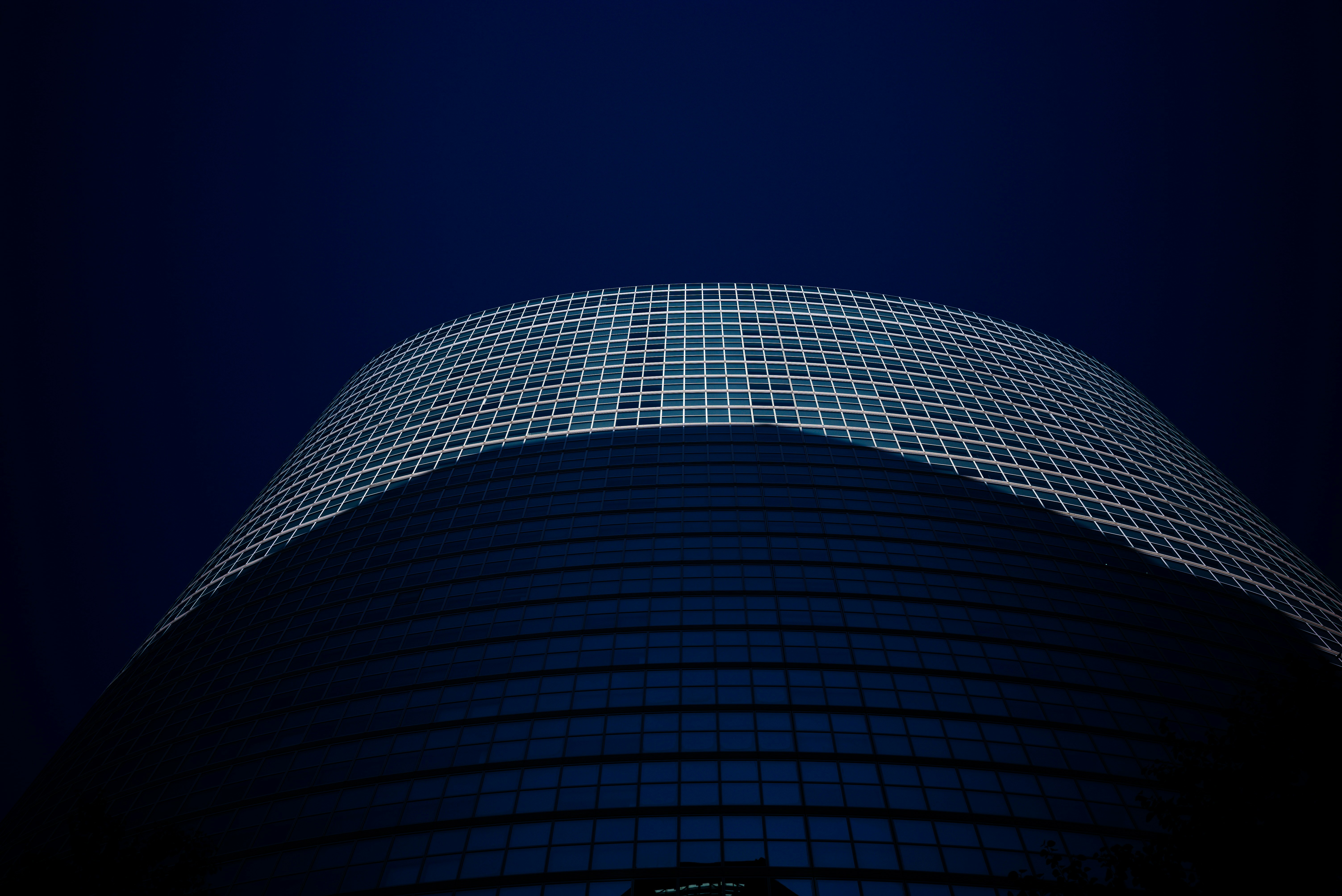 Modern high-rise building with illuminated windows set against a deep blue sky.
