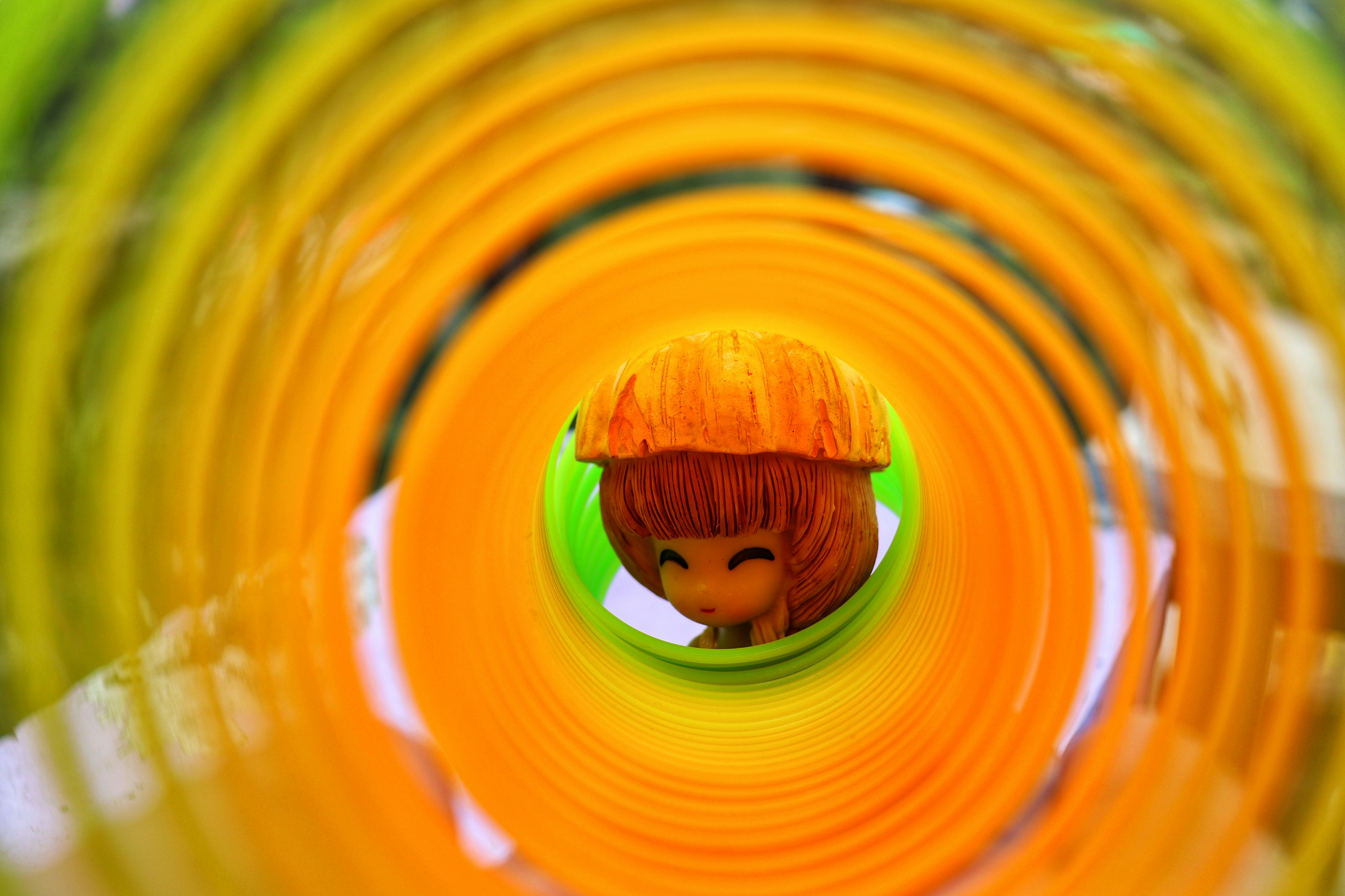 A cheerful character peeks through a vibrant orange spiral toy, surrounded by playful colors and shapes. The scene evokes a sense of joy and nostalgia.