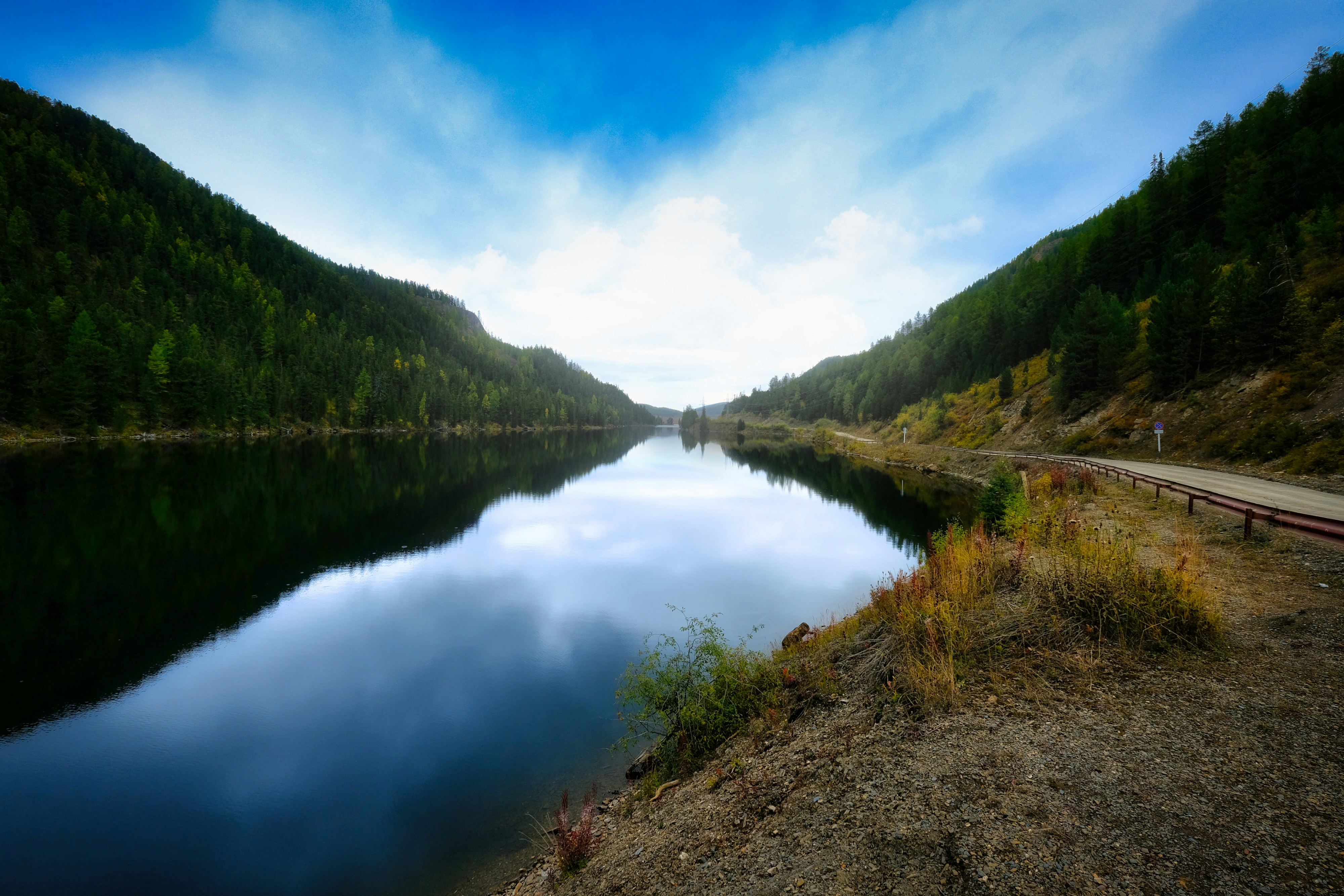 Serene lake reflecting blue sky and lush green hills on a clear day.