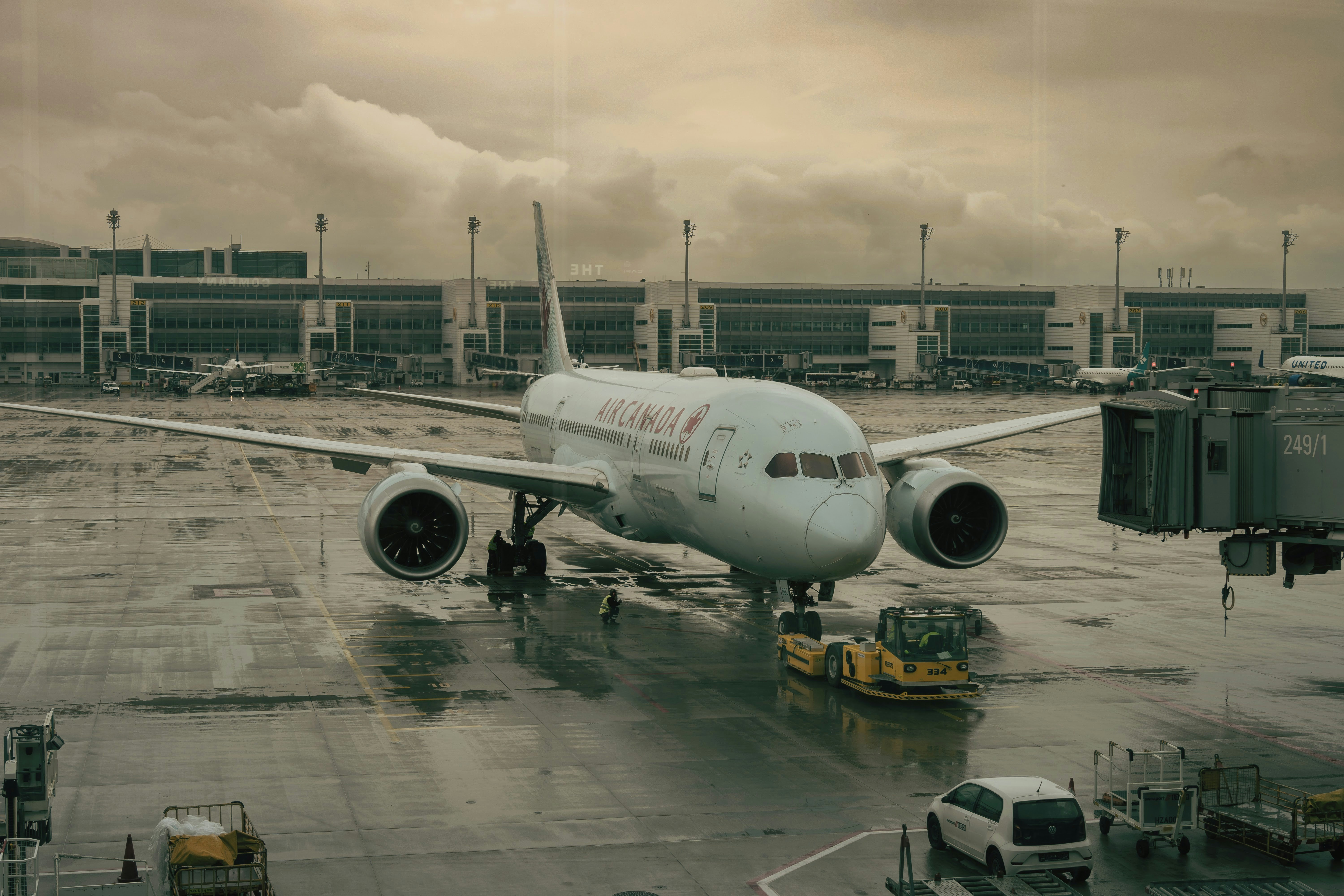 Airplane parked at the terminal with ground crew preparing for departure on a rainy day.