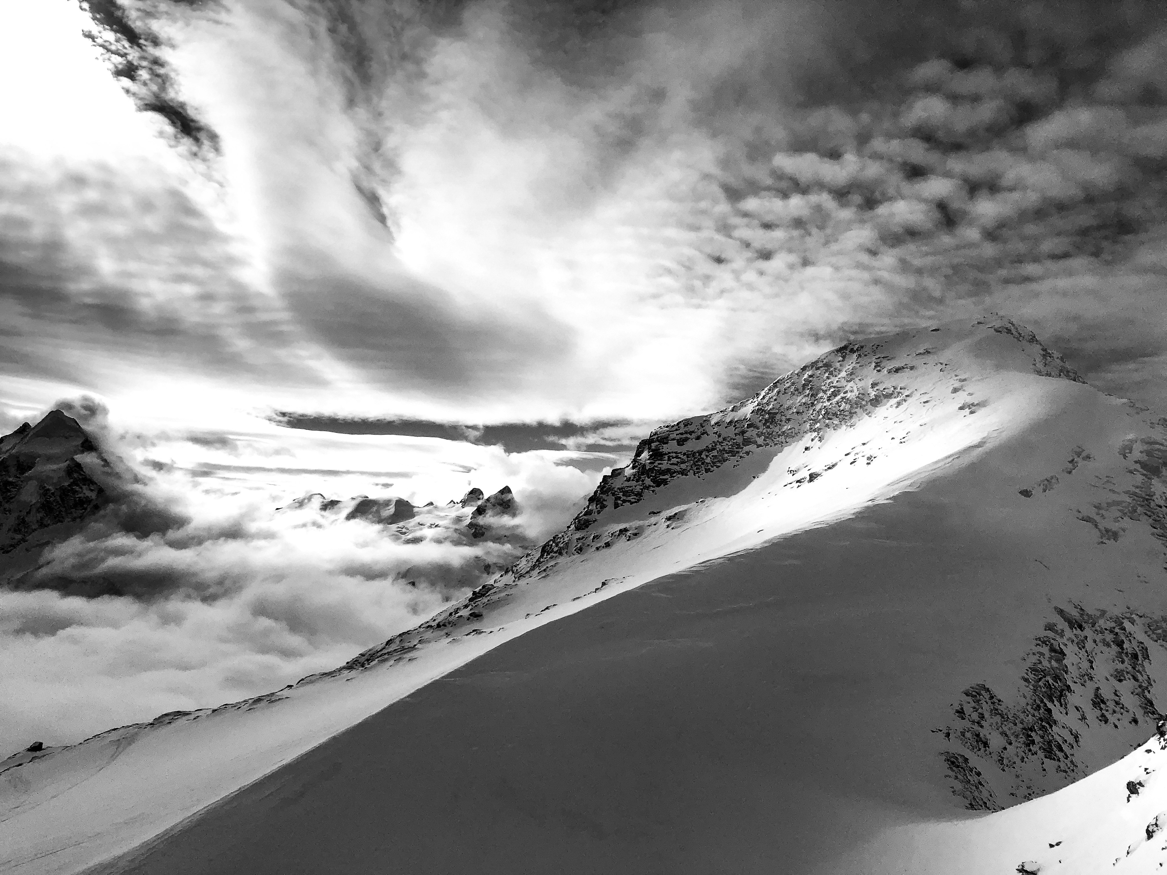 Dramatic black and white landscape showcasing snow-covered peaks under a swirling sky, evoking a sense of tranquility and majesty.