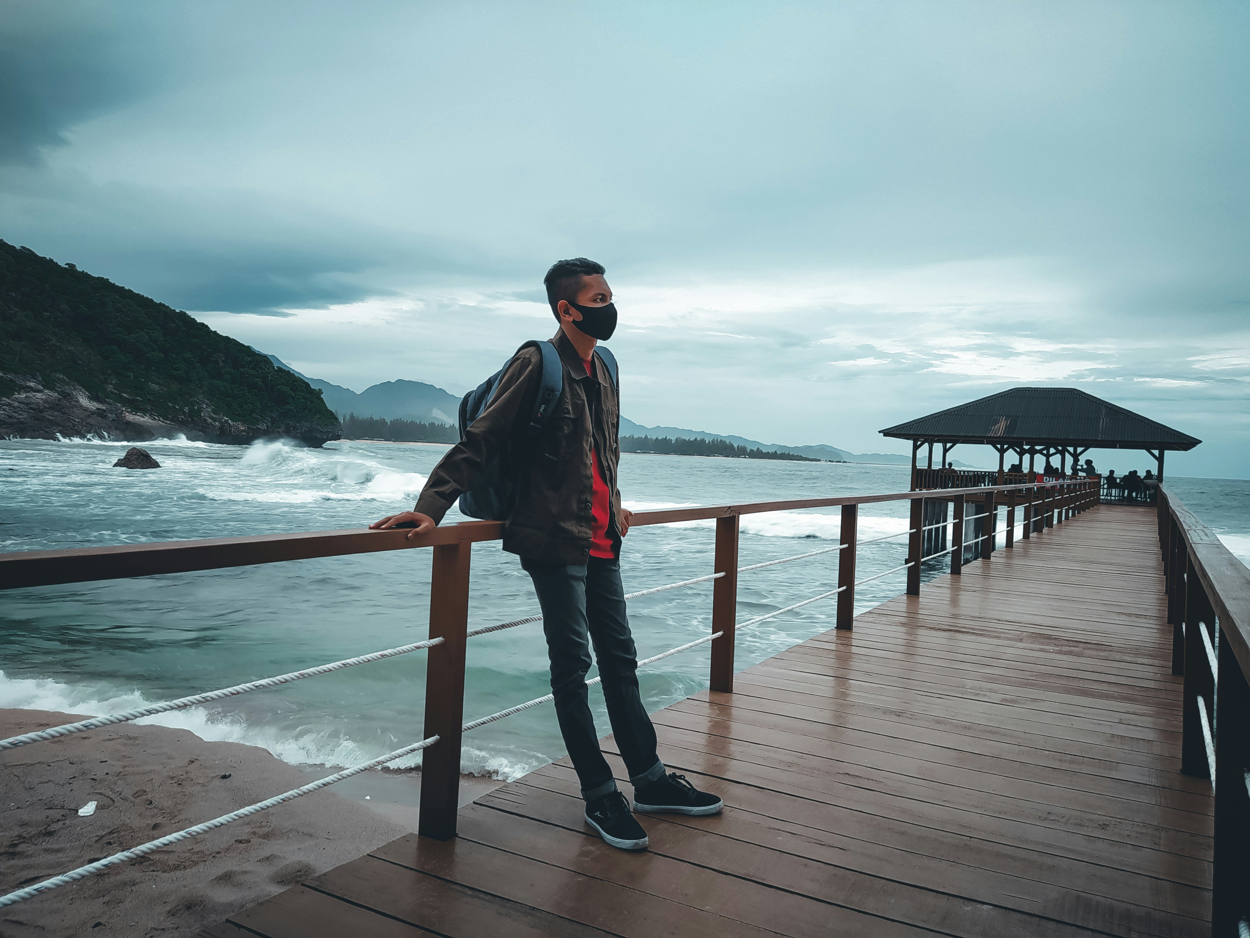 Masked Wanderer on a Windward Pier Under Overcast Skies