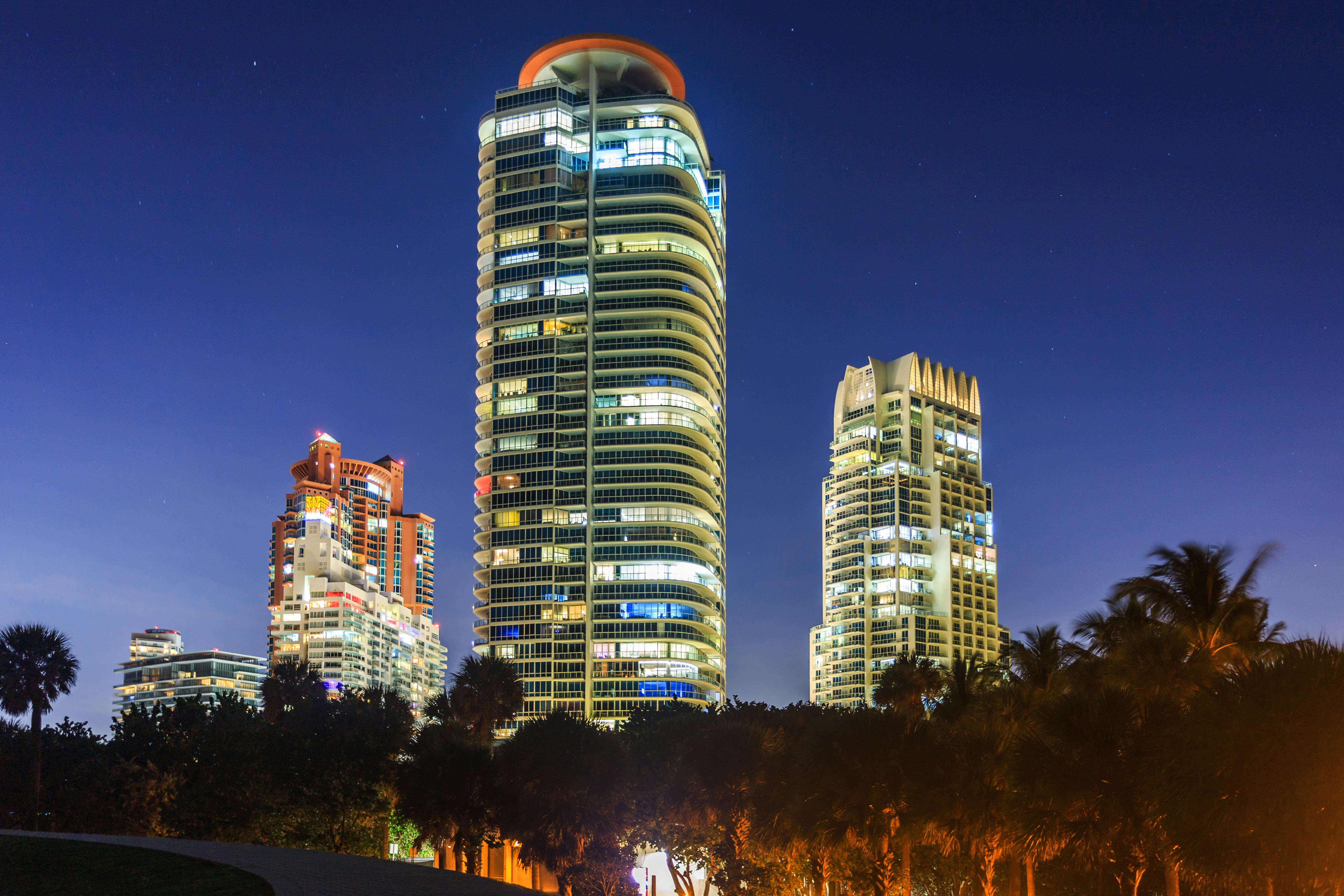 Moonlit Skyline: A Trio of Glass Towers Rising Over Nightime Palm Shadows