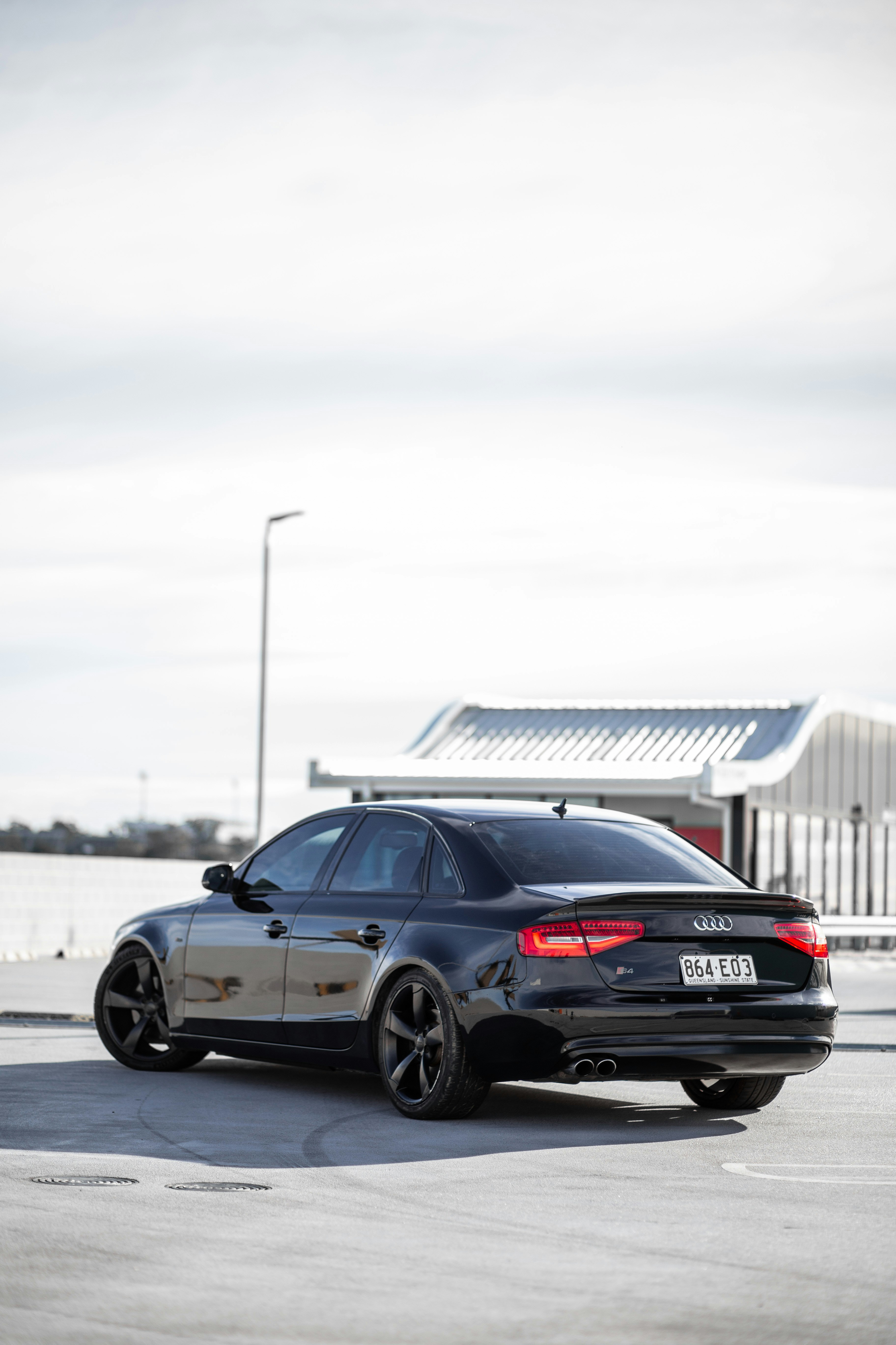 Midnight Audi Sedan on a Rooftop Parking Deck: Rear-Quarter Stance Under Open Sky