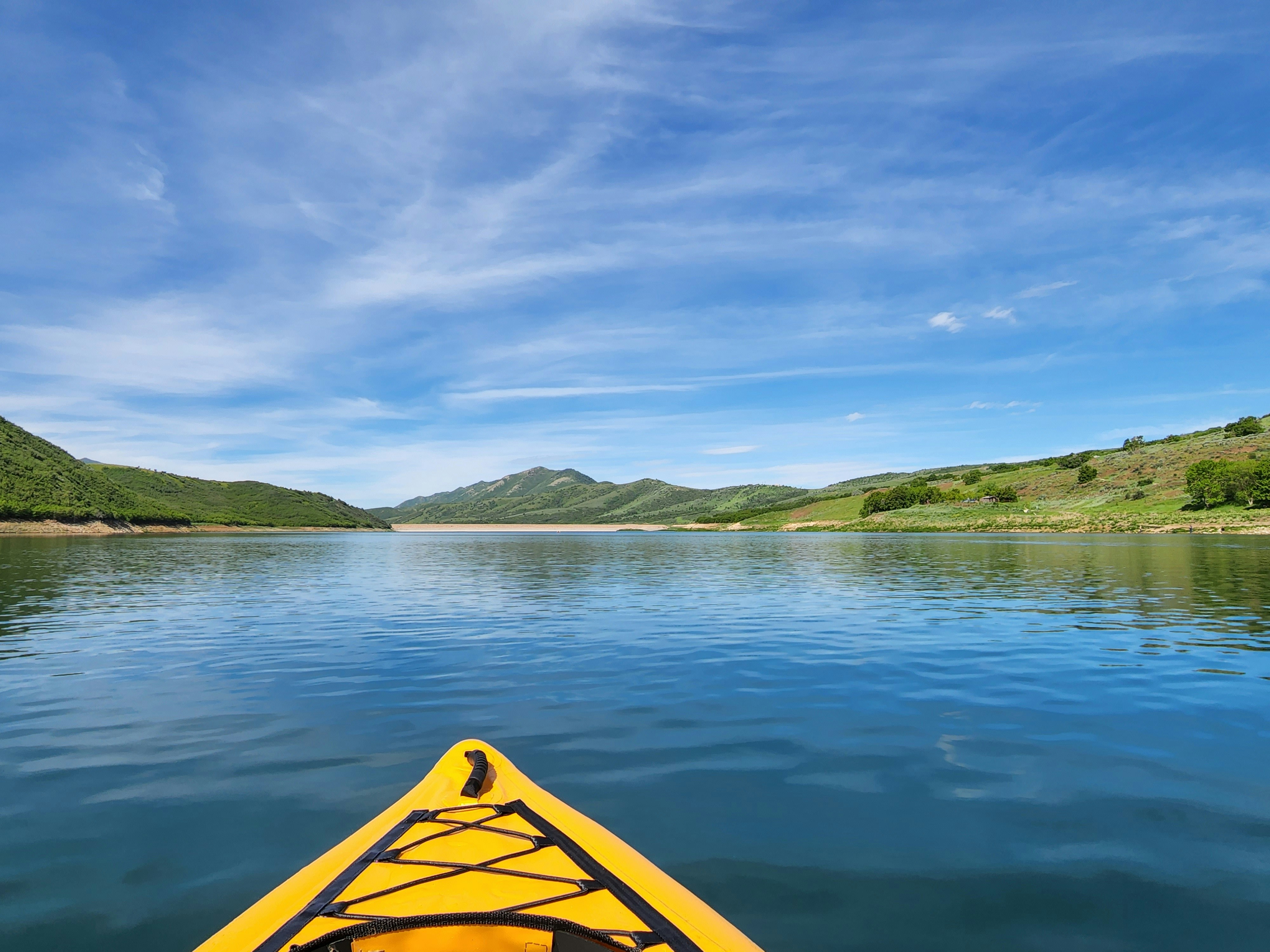 A vibrant yellow kayak glides across a tranquil lake, surrounded by lush green hills and a clear blue sky. The scene captures the essence of peaceful outdoor adventure.