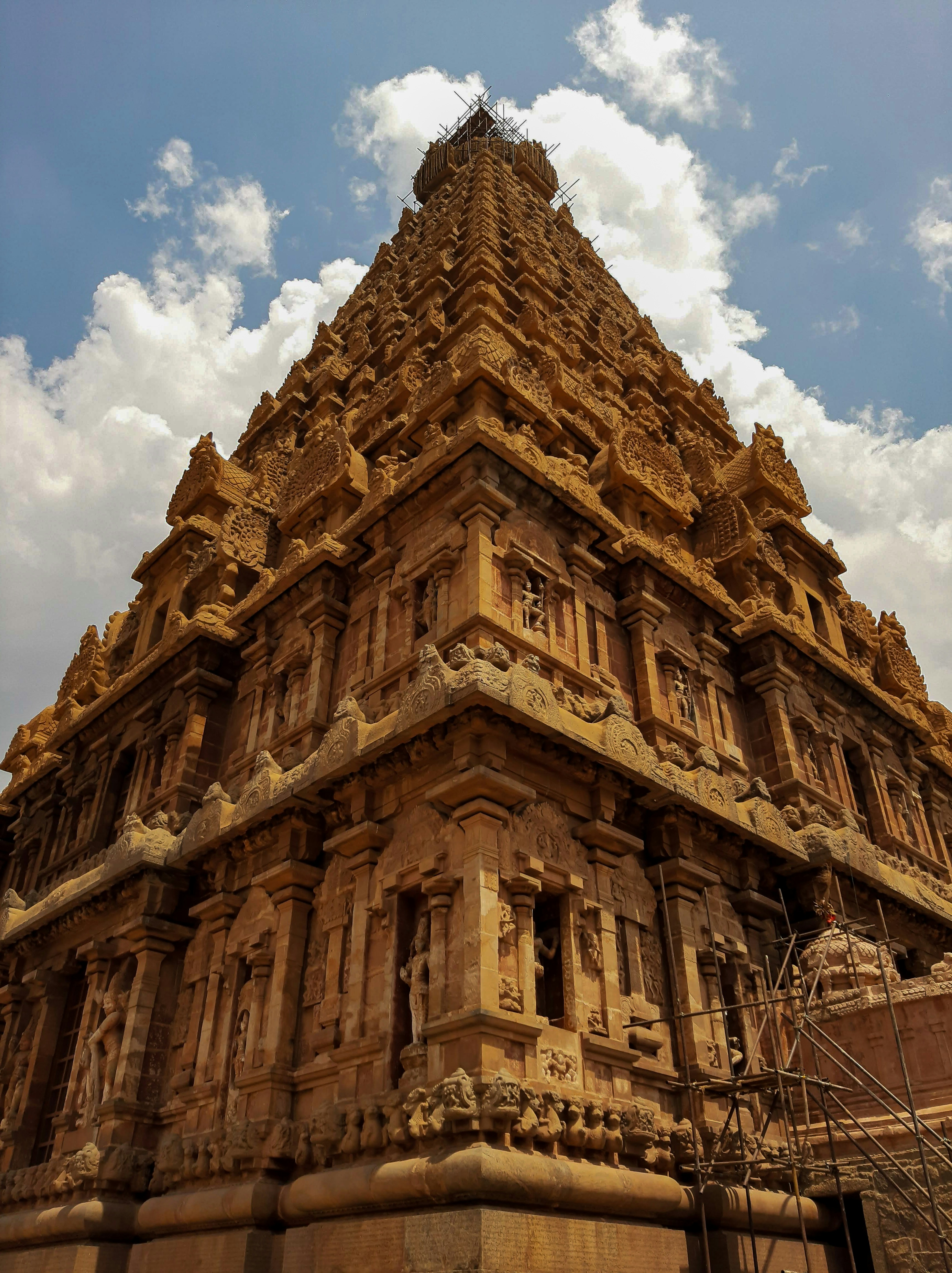 Intricate stone carvings adorn the towering structure of a historic temple, showcasing architectural grandeur against a backdrop of dynamic clouds.
