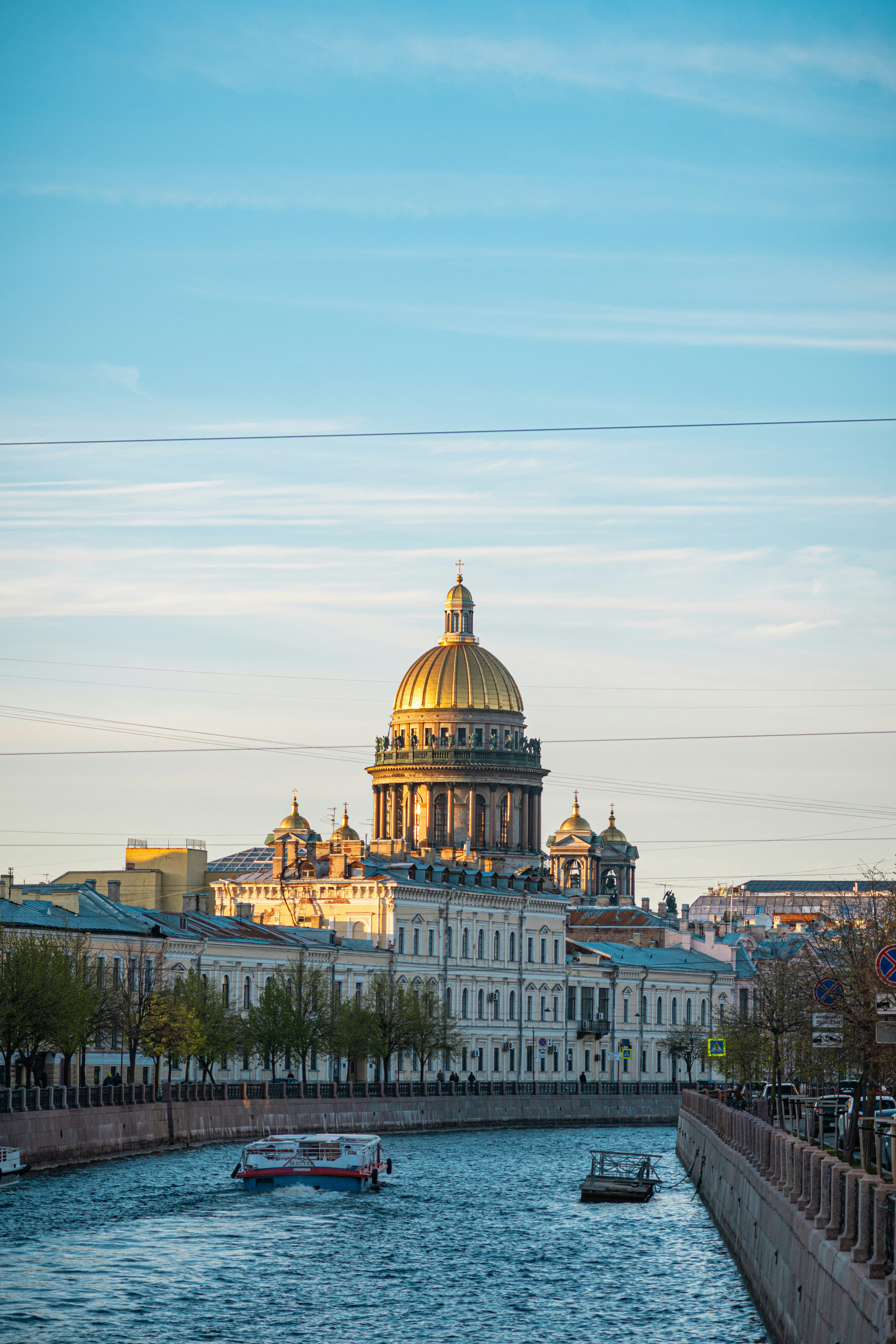 Historic cathedral with a striking golden dome rises above the river, framed by trees and city architecture. The scene captures the essence of urban life and architectural beauty.