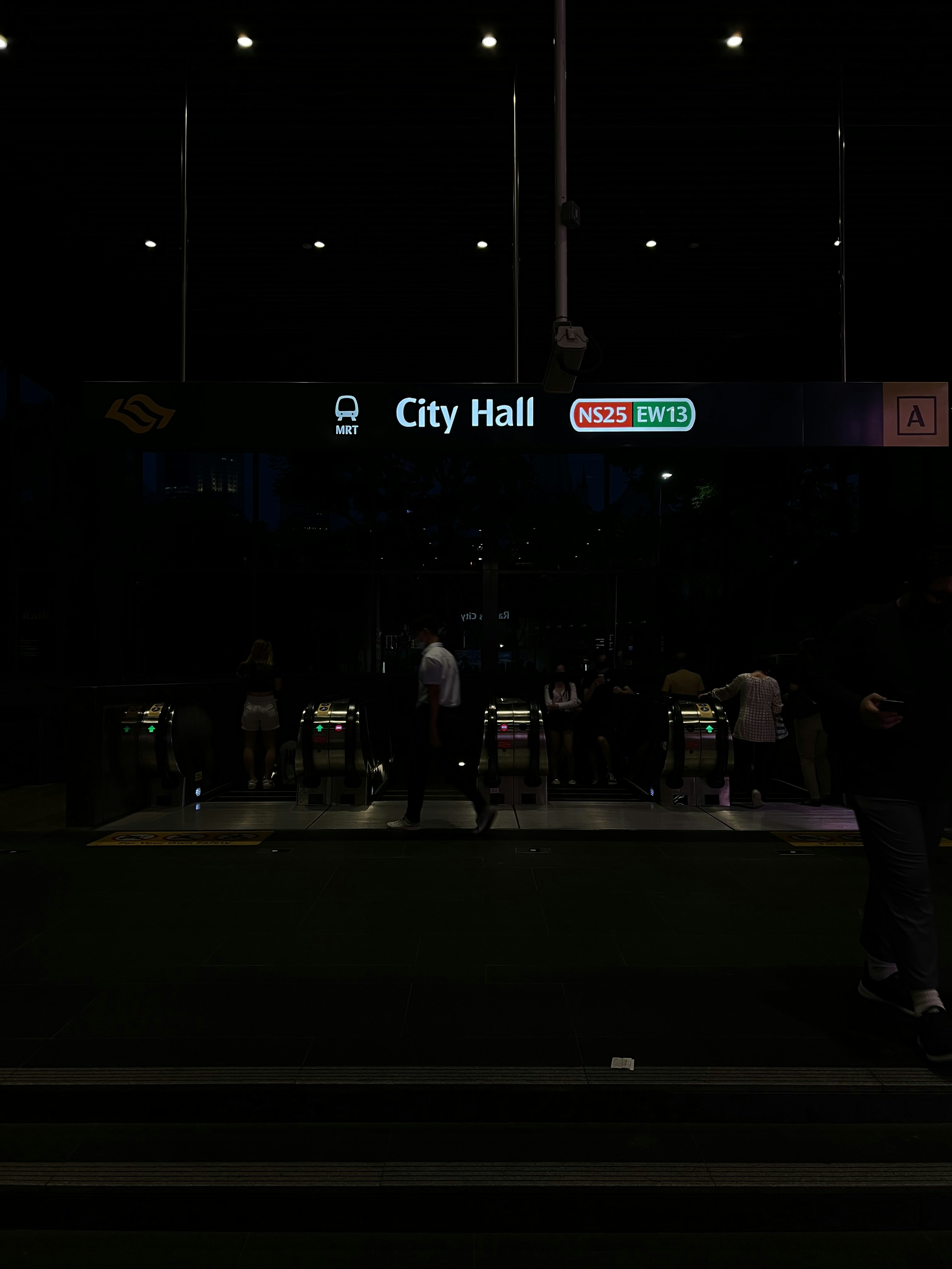 Illuminated City Hall sign at a bustling subway entrance, with commuters passing through. The scene captures the vibrancy of urban transit.