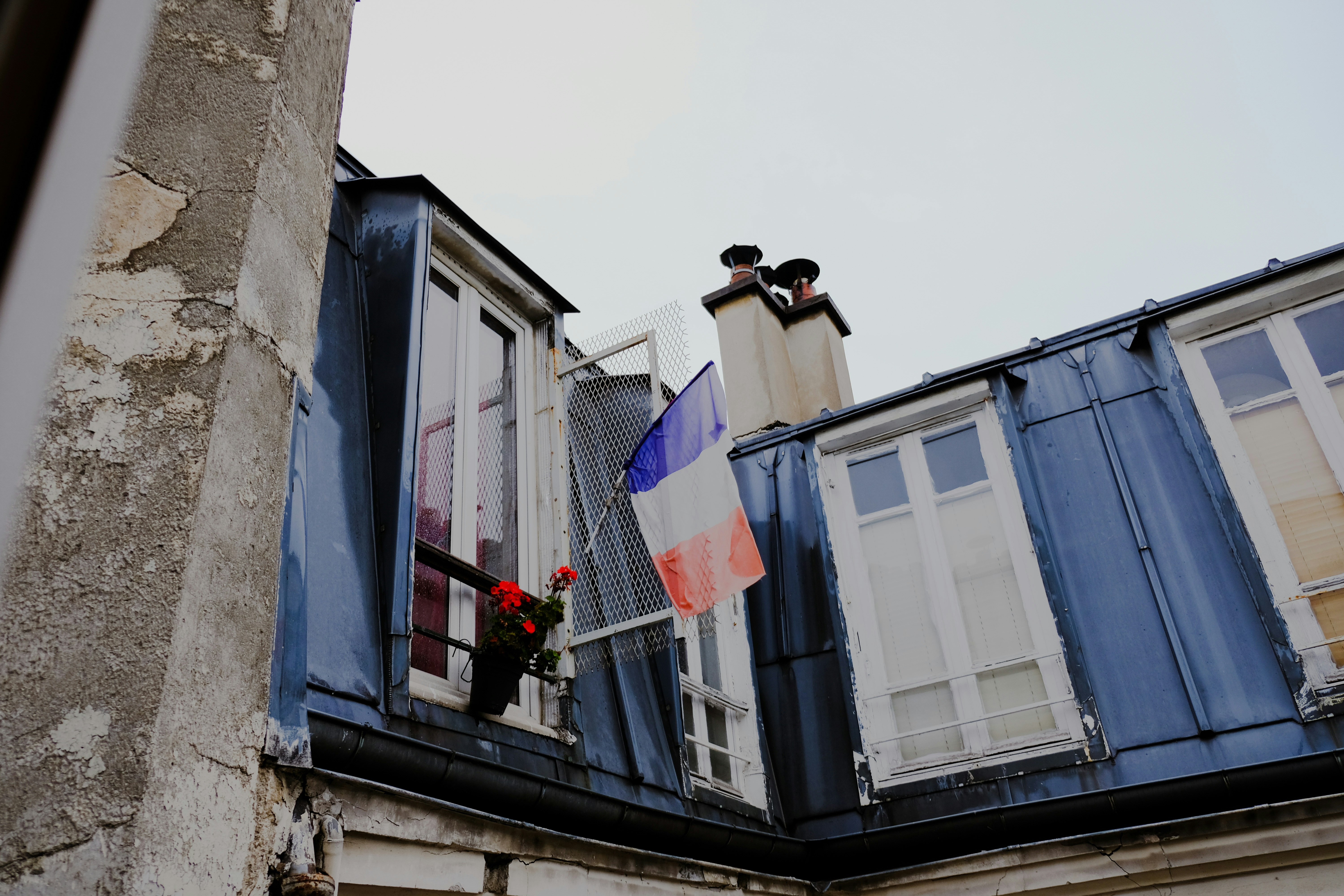 French flag fluttering beside flower-adorned balcony in a quaint rooftop setting.