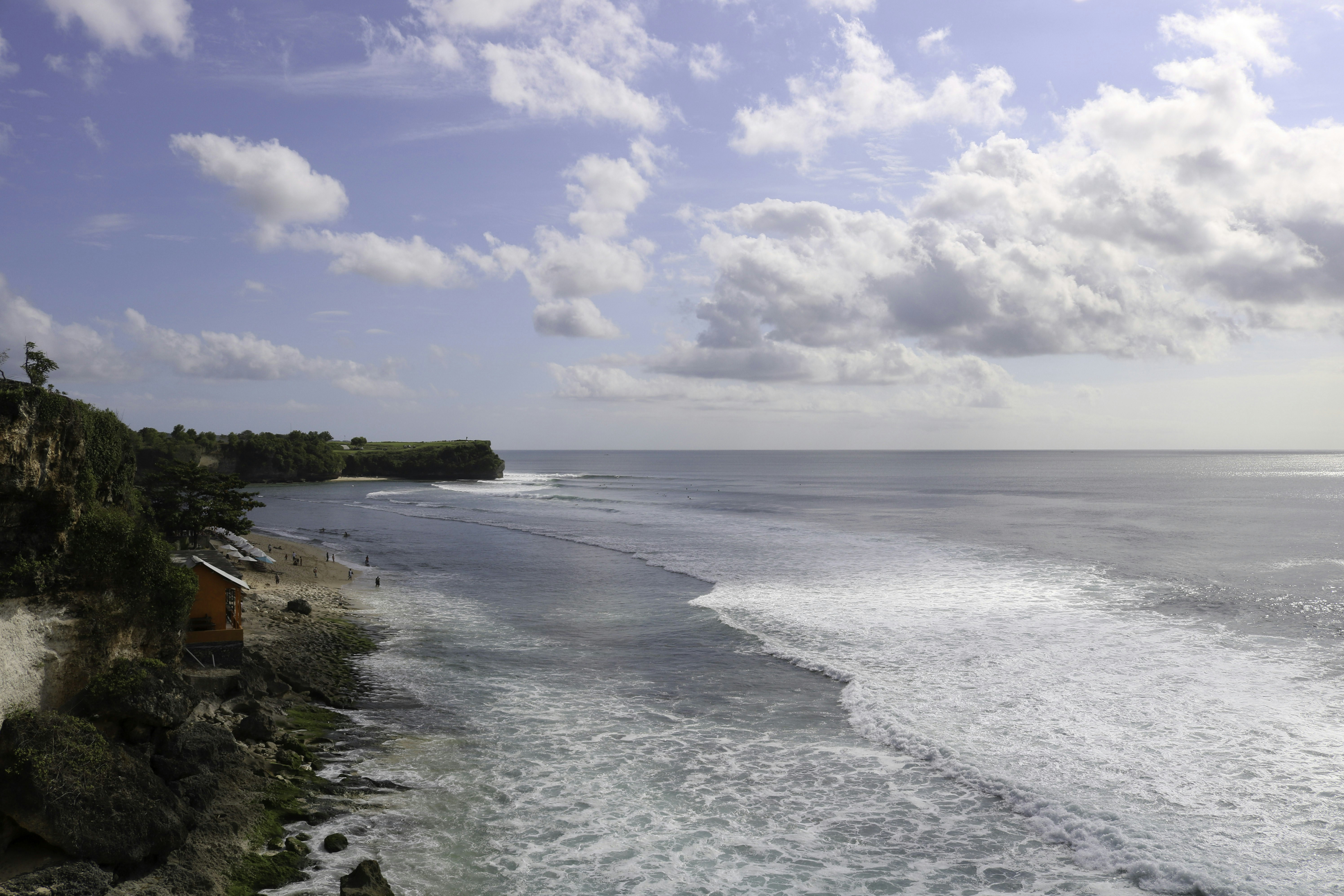 Waves gently lap against a rocky shoreline under a cloudy sky, with a hint of greenery in the background. The scene captures the tranquil essence of a coastal escape.