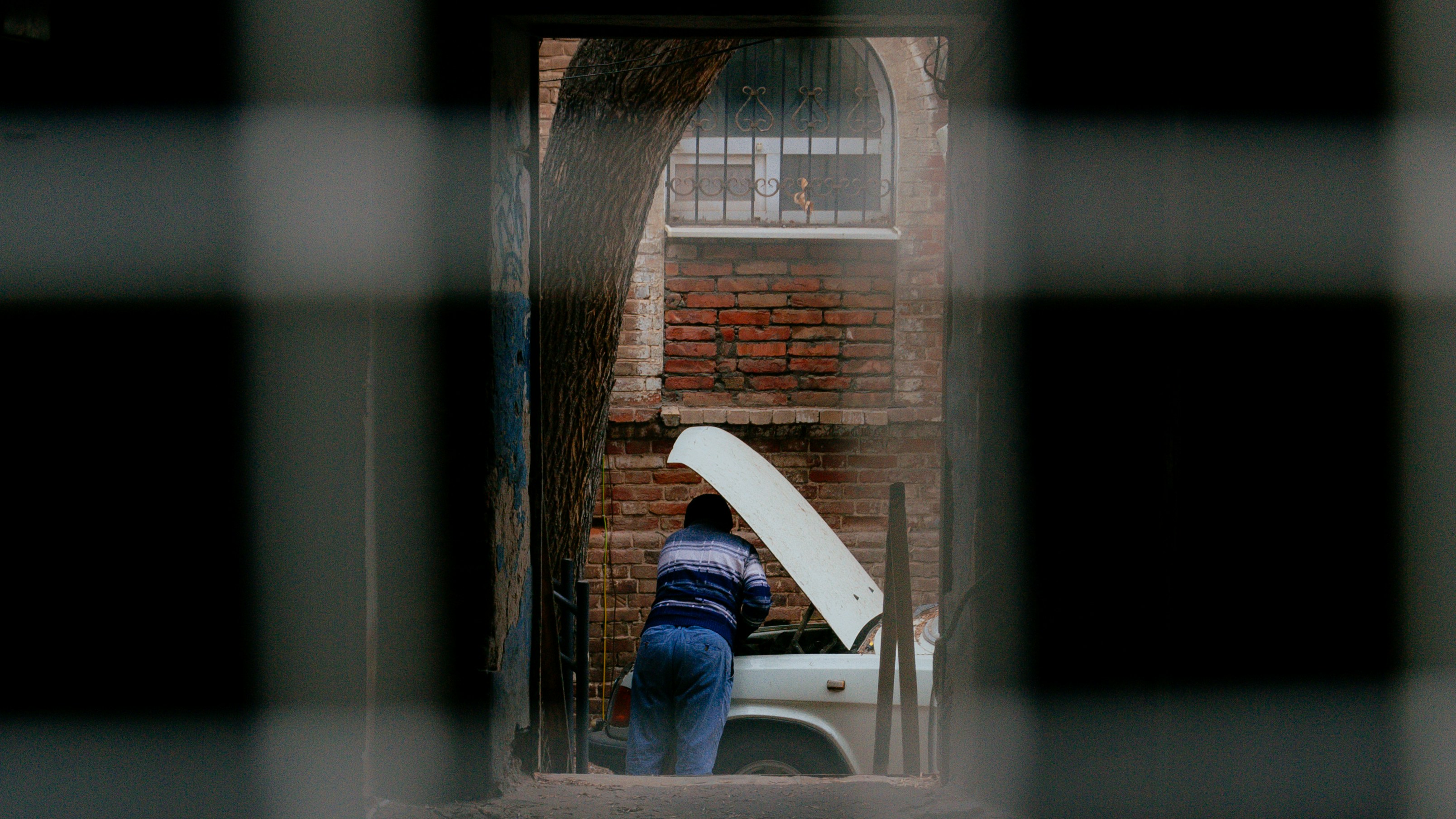 Person inspecting a car engine beneath an archway in a brick alley.