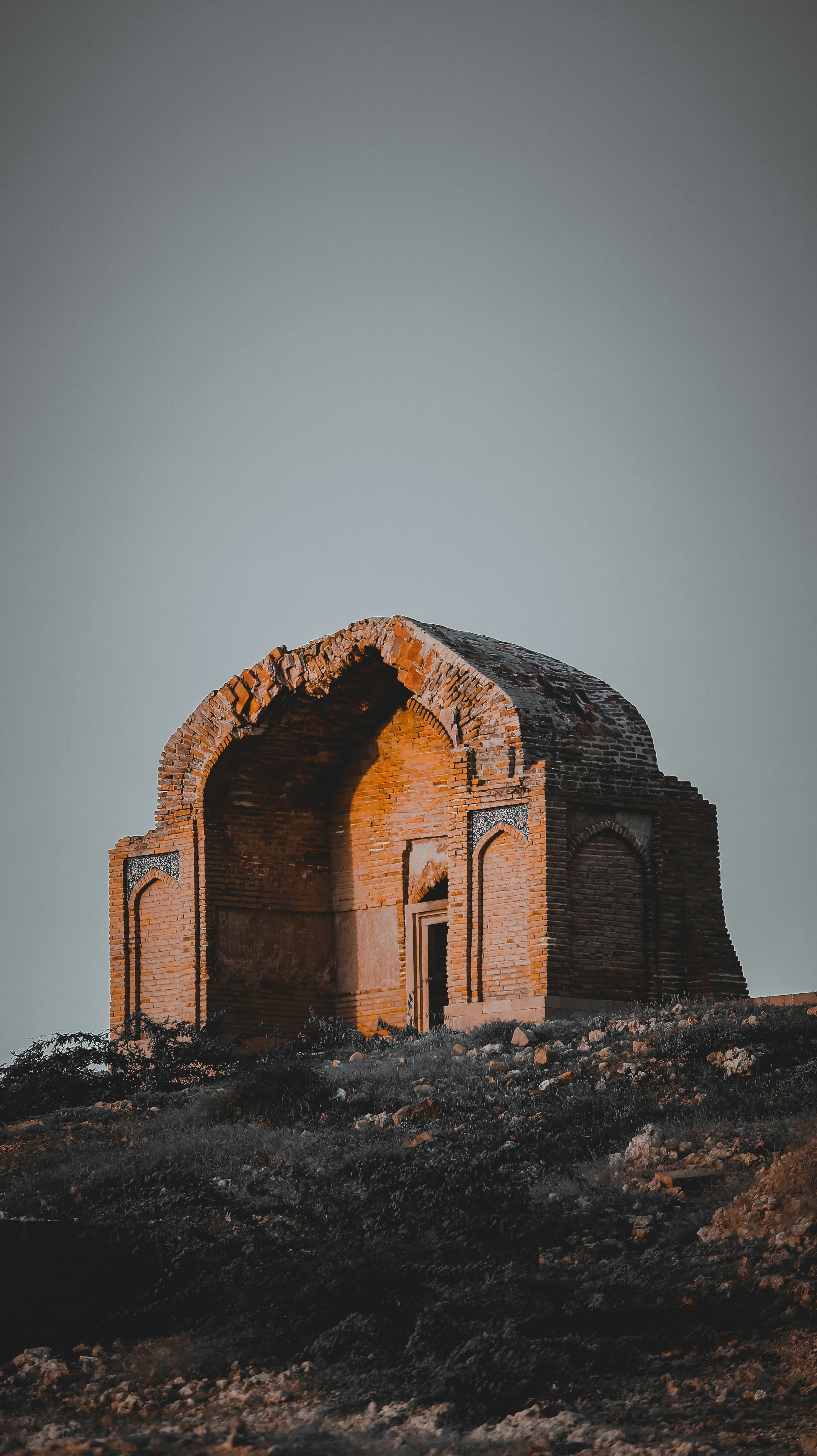 Ancient brick pavilion perched on a hill, illuminated by soft sunlight, surrounded by lush greenery.