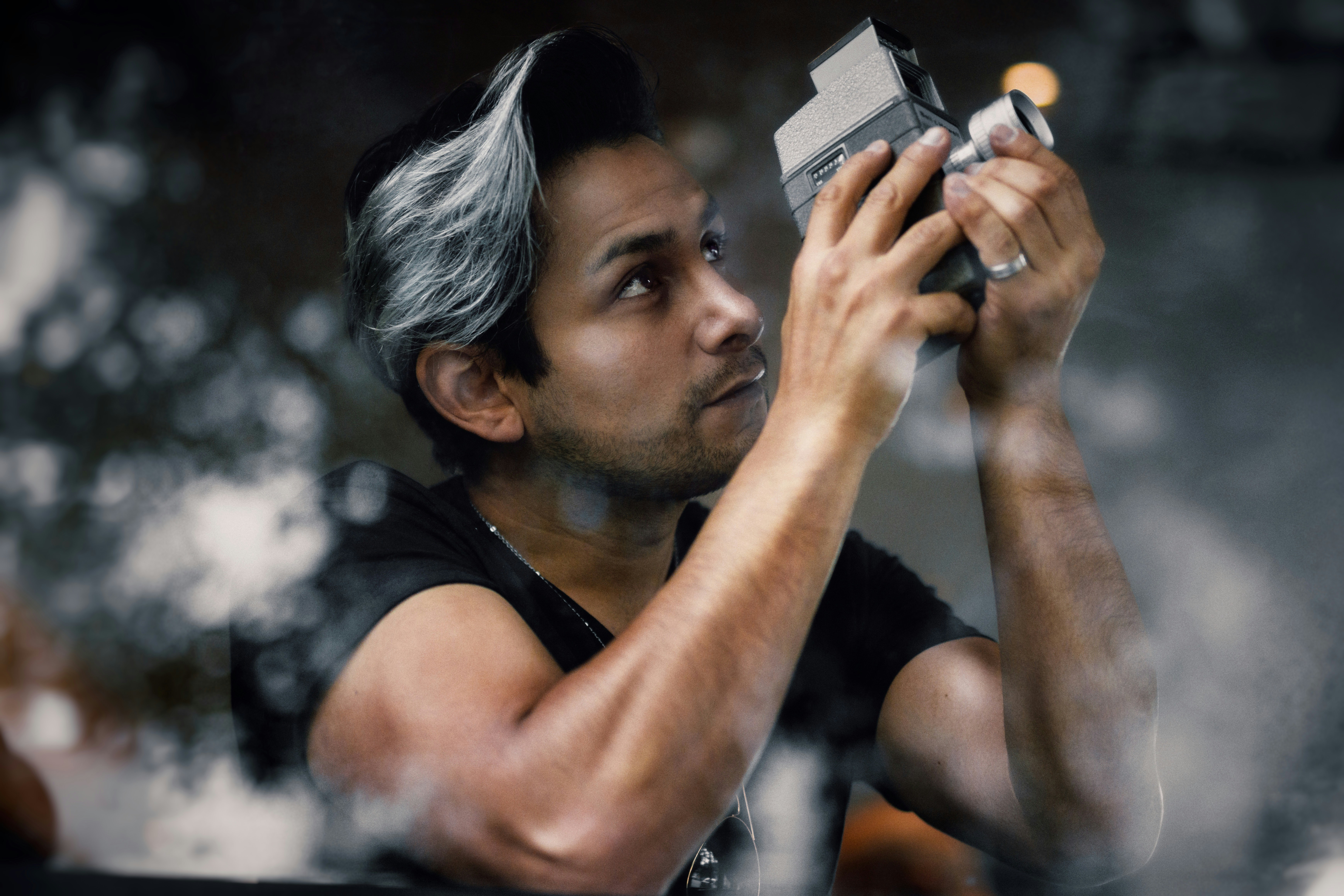 Person holding a vintage camera, gazing upwards through a blurred window reflection.