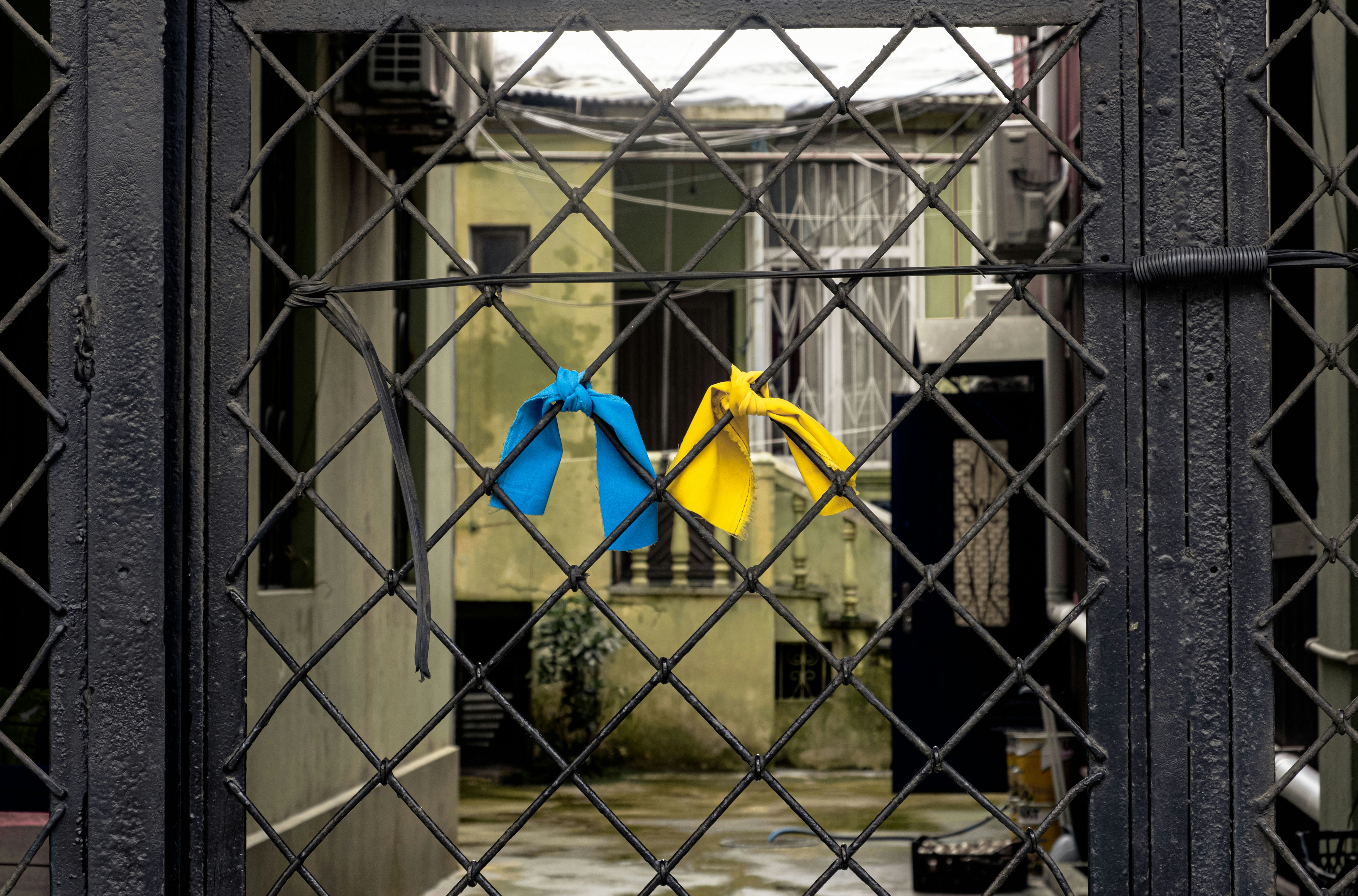 Blue and Yellow Ribbons Framing a Quiet Courtyard Behind the Gate