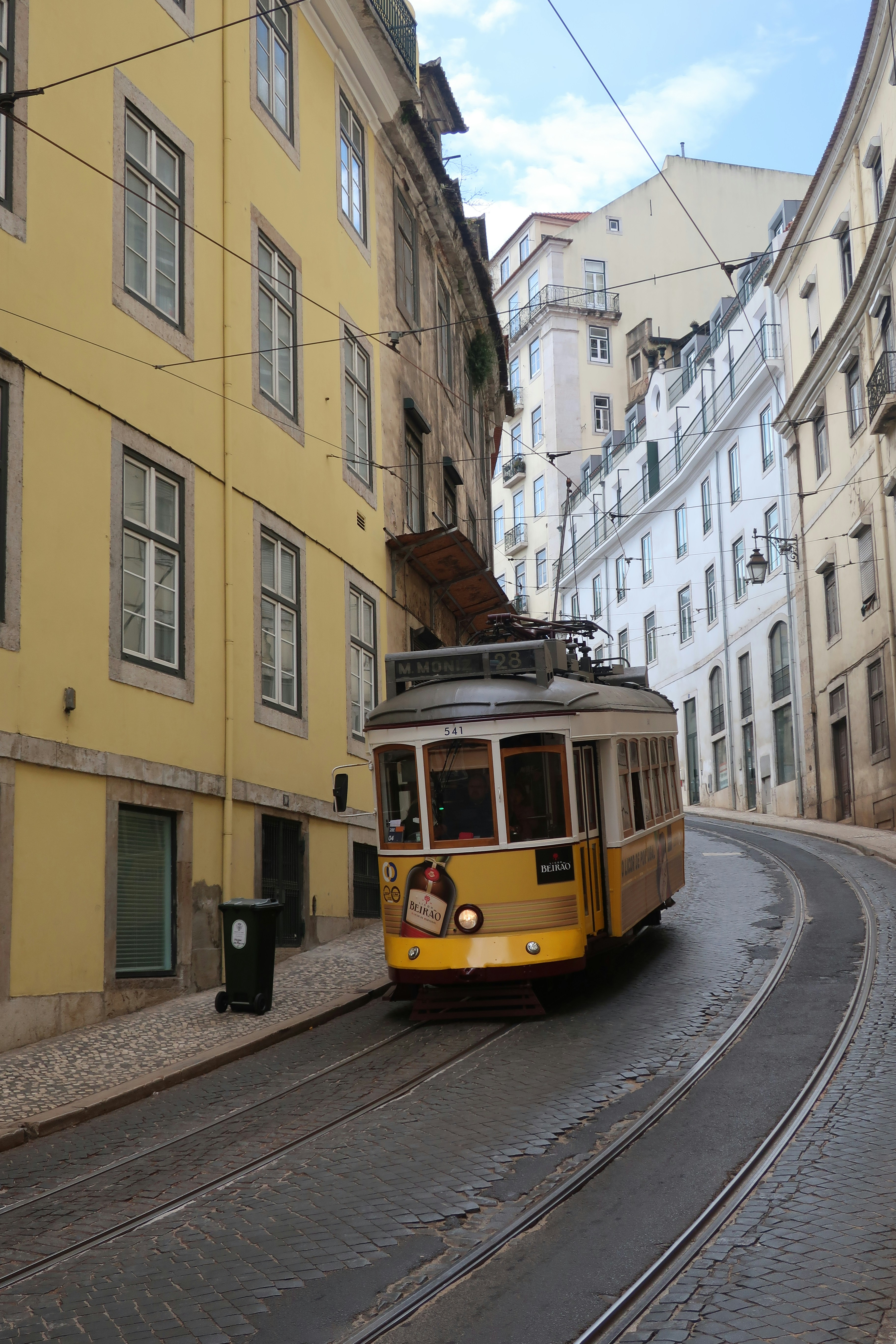 Vintage yellow tram navigating a narrow, cobblestone street lined with colorful buildings in Lisbon.