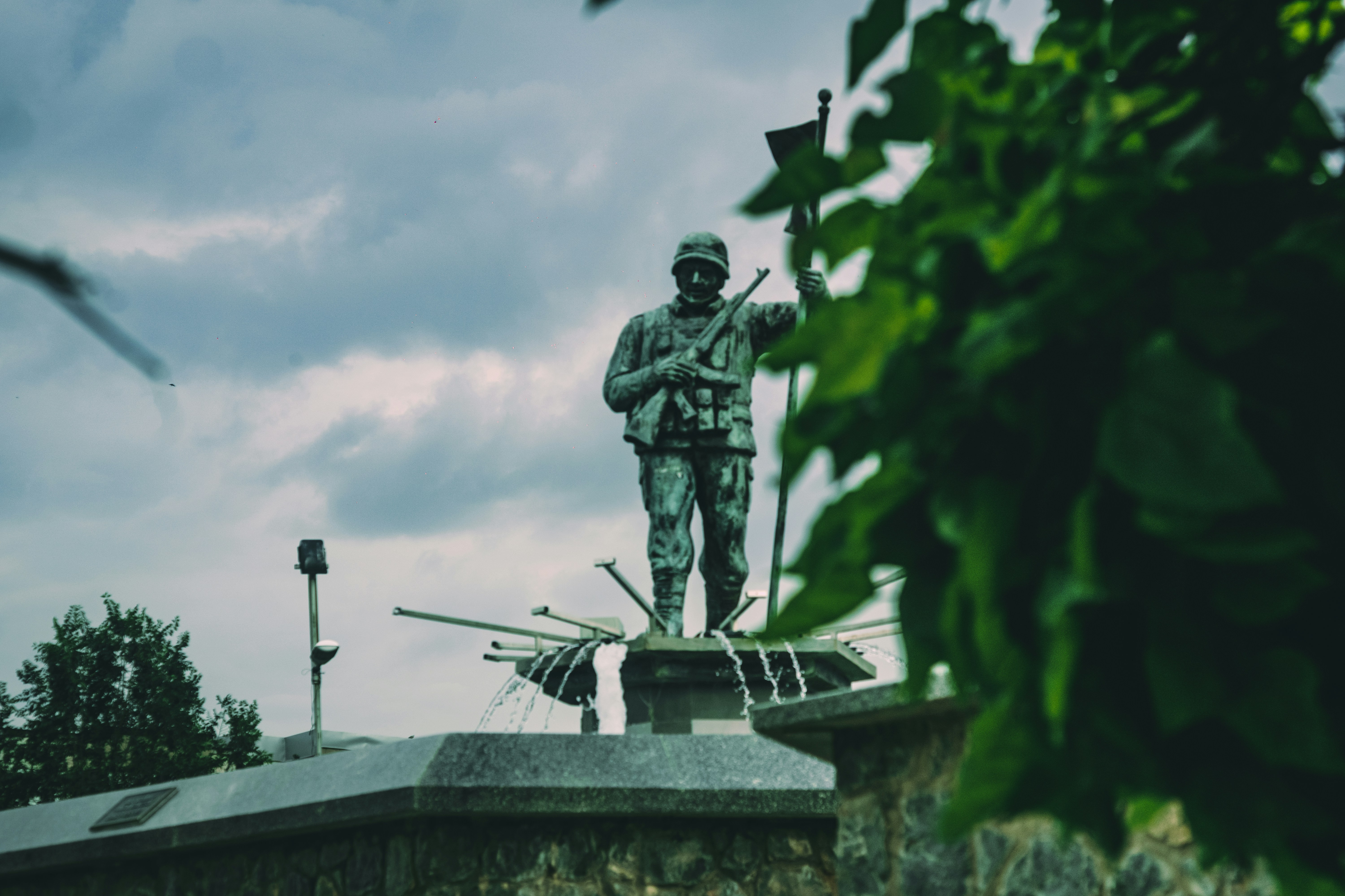 Rifleman Sentinel Above the Pedestal, Framed by Greenery and a Cloudy Sky