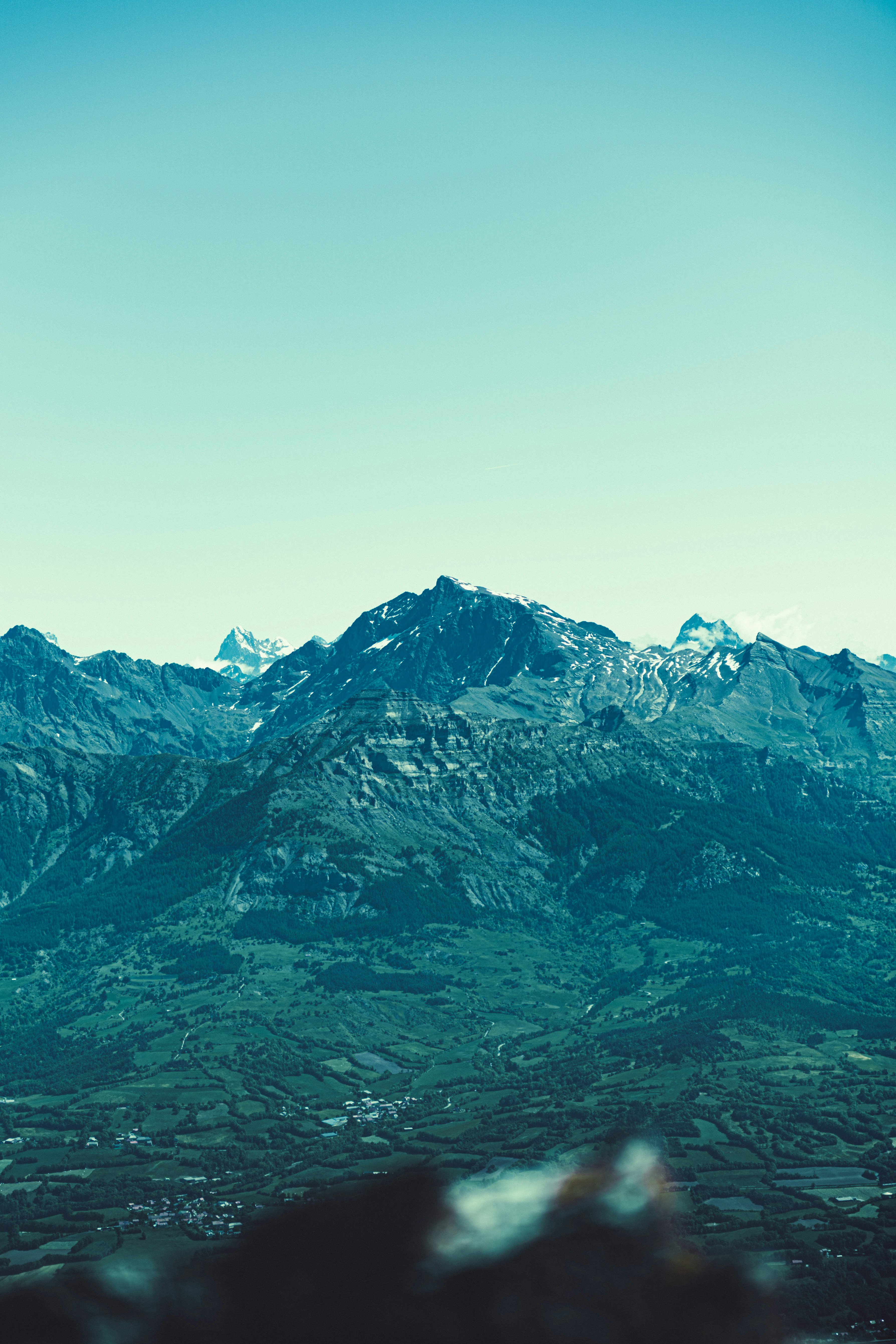 Snow-capped mountains rise majestically against a clear blue sky, showcasing the rugged beauty of nature's landscape.