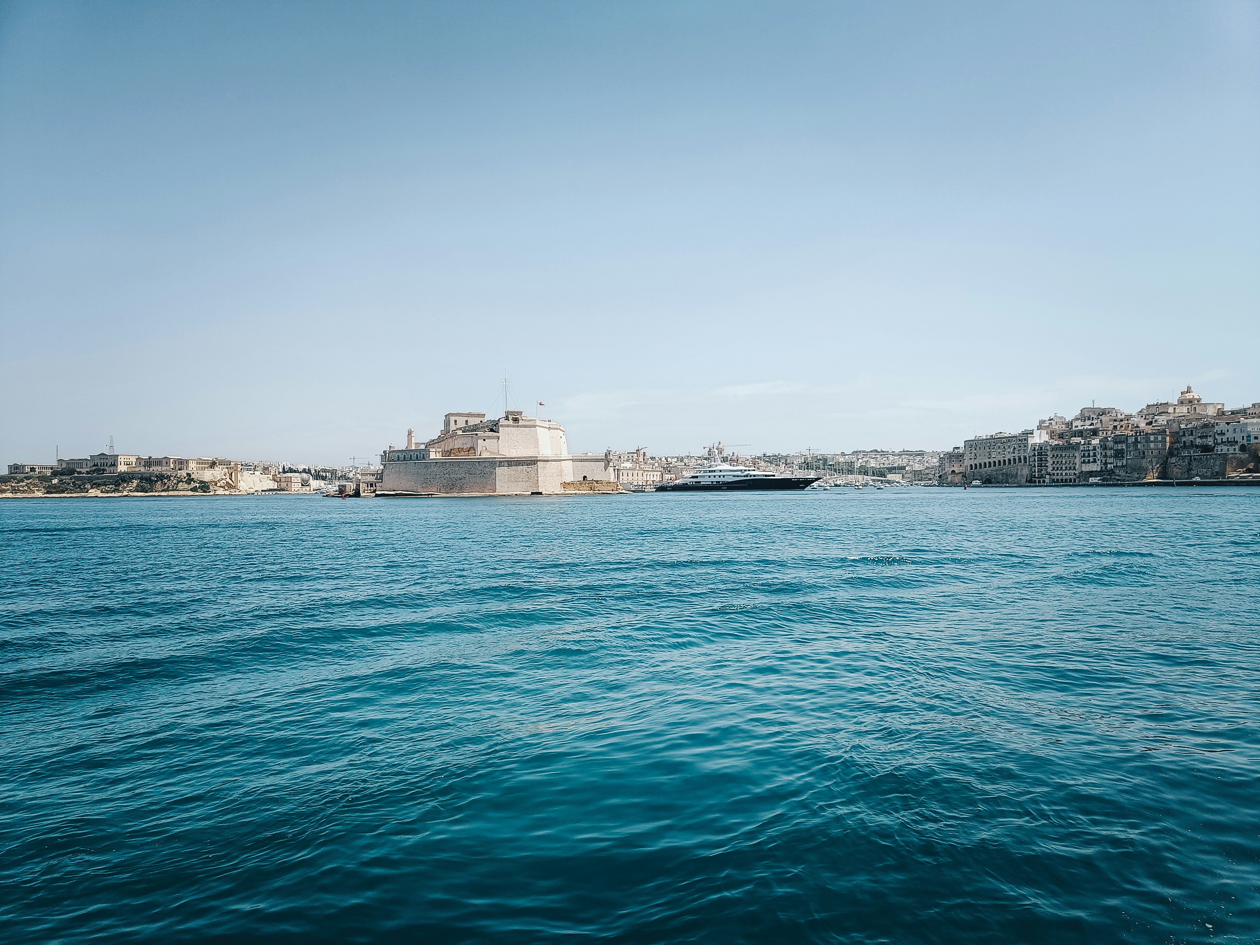 A tranquil harbor scene featuring a large structure and yachts against a clear blue sky, showcasing the essence of coastal living.