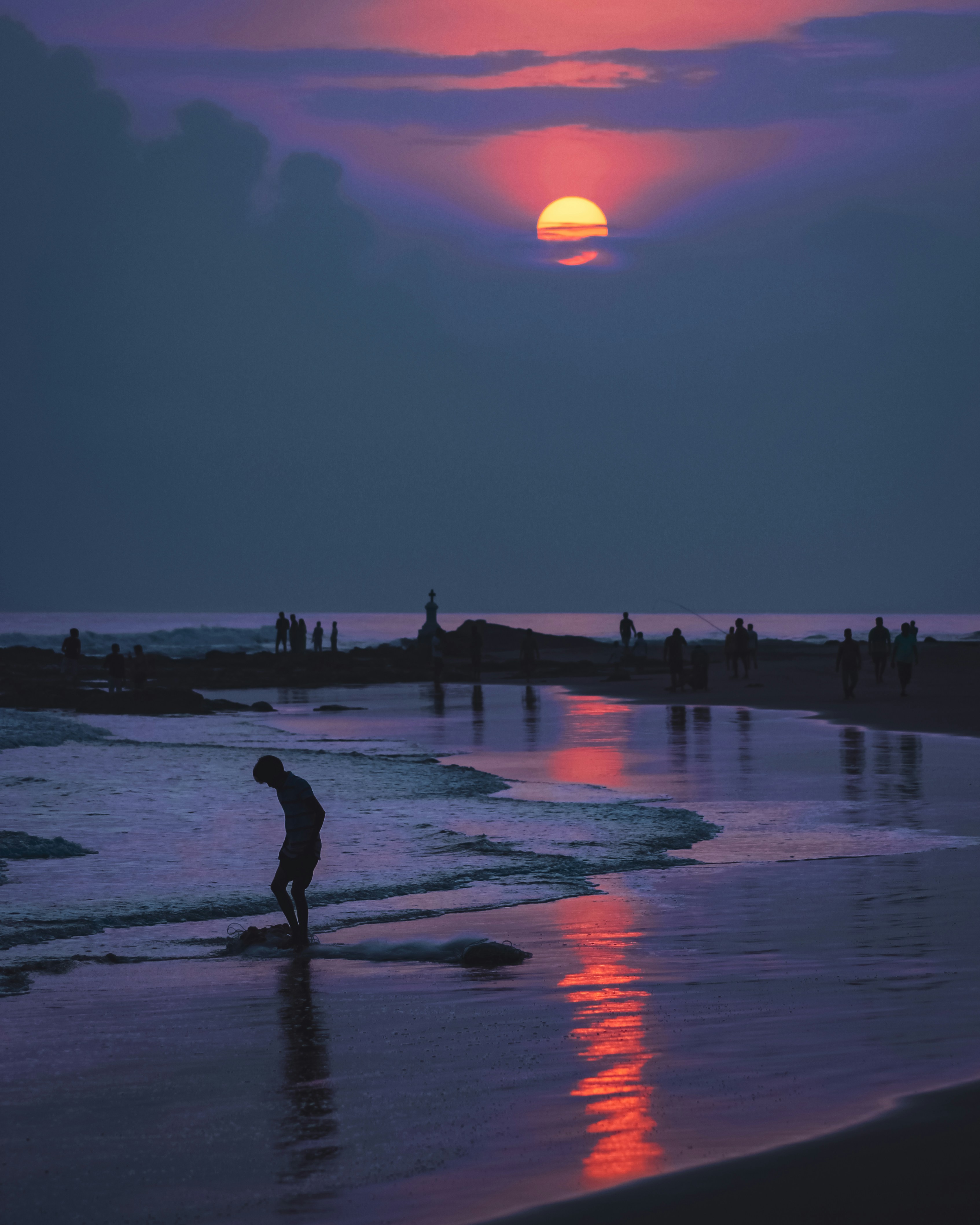 A sunset shot with the silhouette of a  fisherman and some more people in the background.