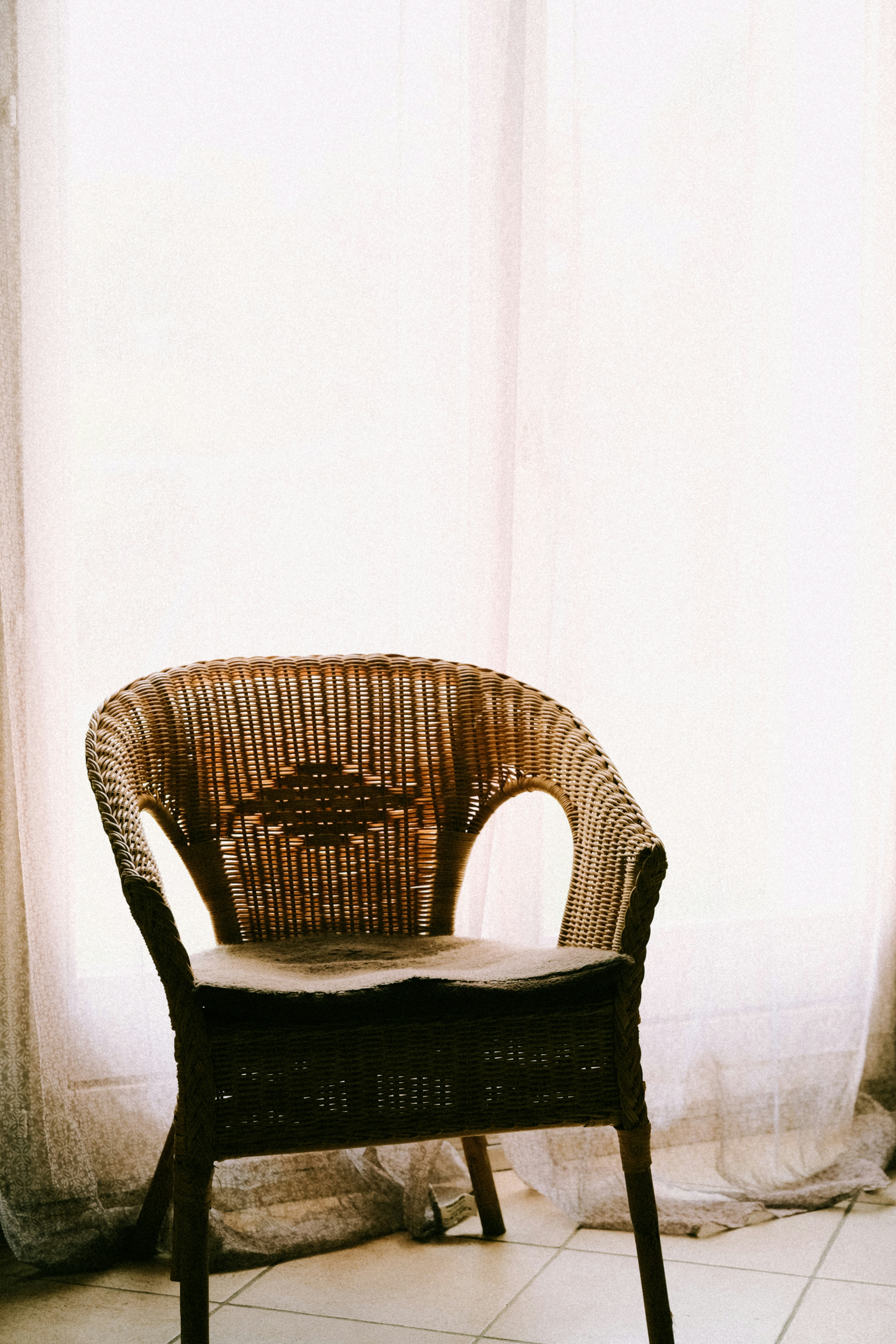 A woven chair sits gracefully by a sunlit window, surrounded by soft, flowing curtains. The scene invites tranquility.
