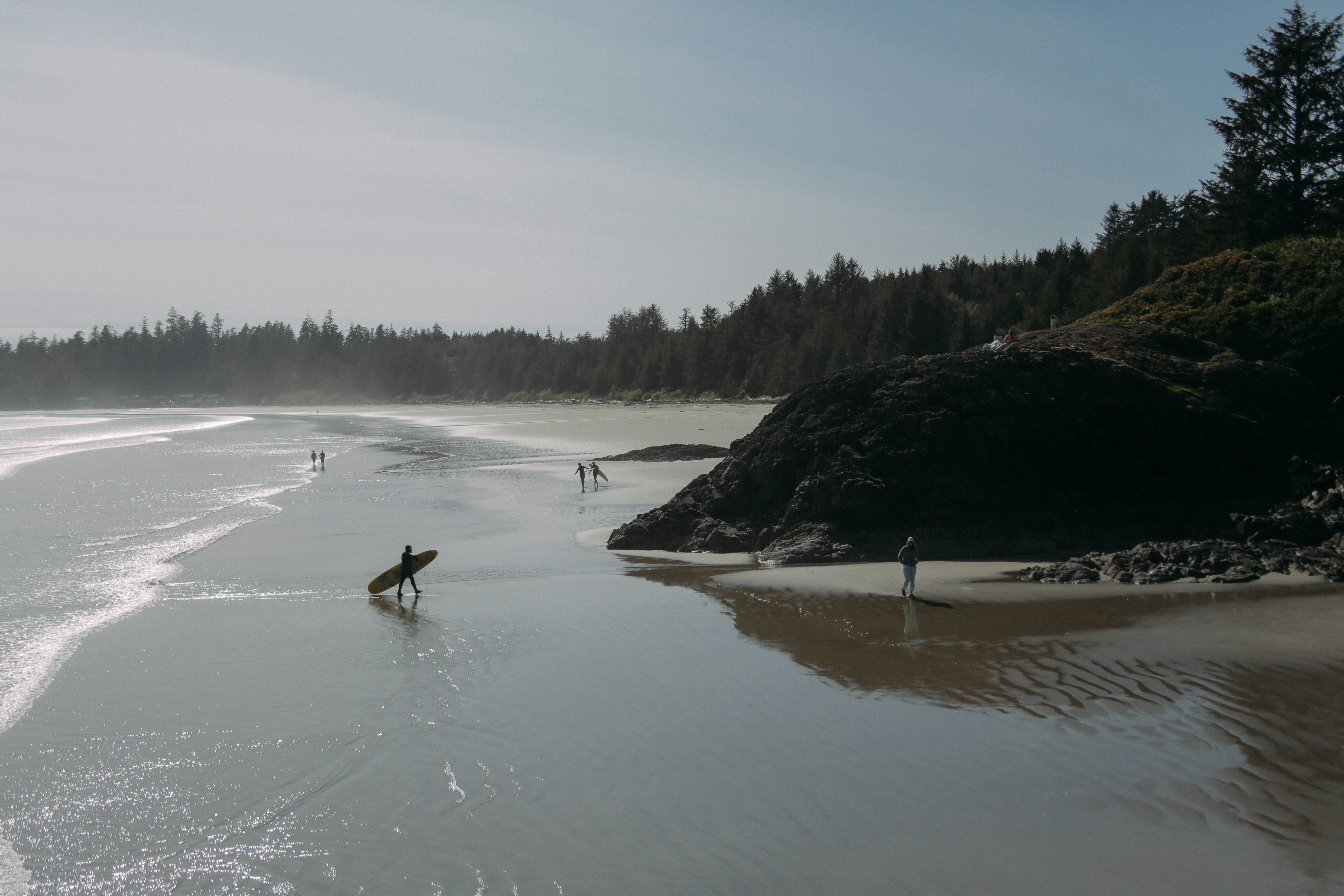 Surfers navigating the gentle waves along a tranquil beach, framed by rocky outcrops and lush greenery. The scene captures the essence of a peaceful day by the ocean.