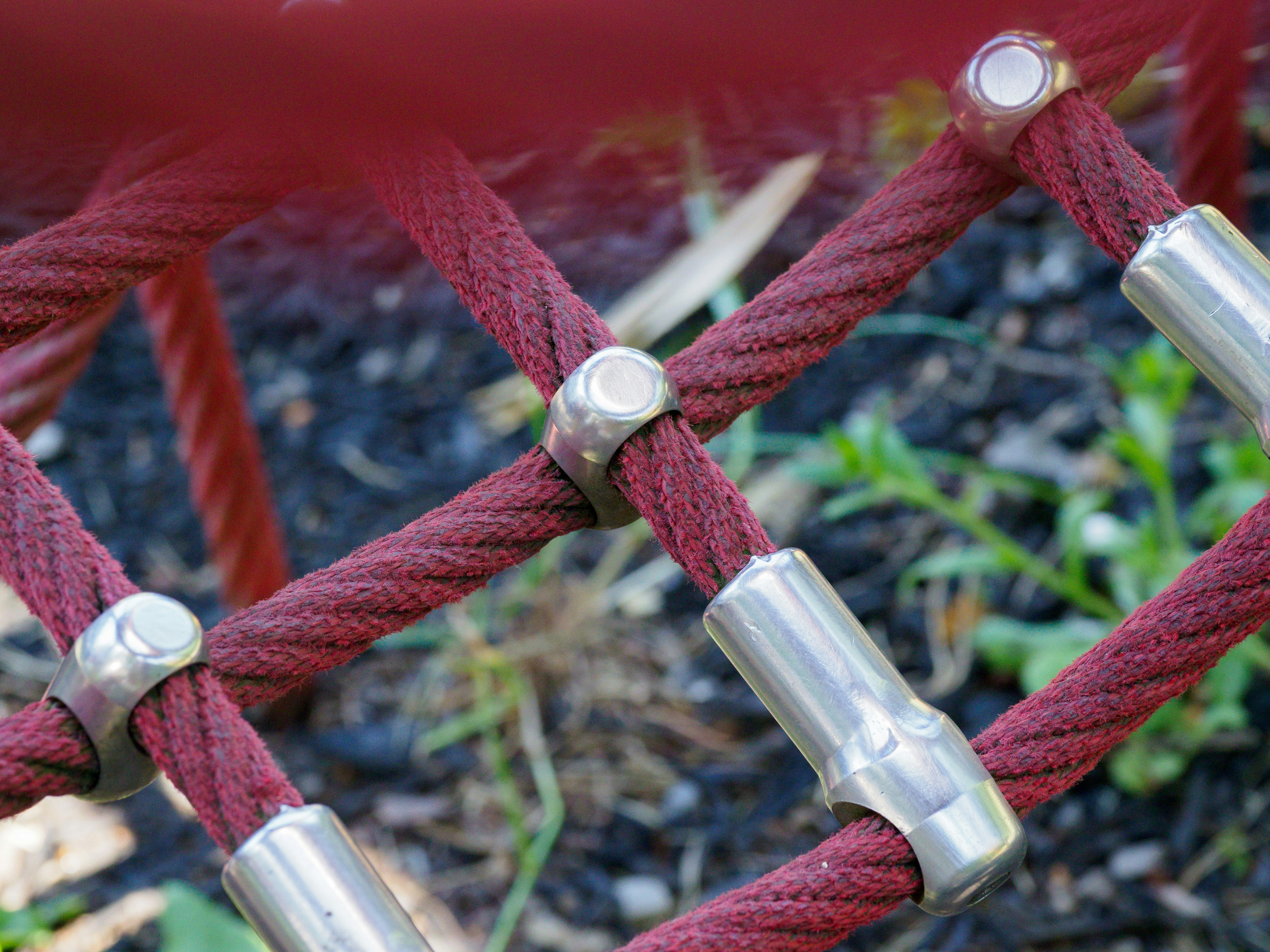 Close-up of intertwined red rope and metallic connectors, showcasing intricate details and textures in a playground setting.
