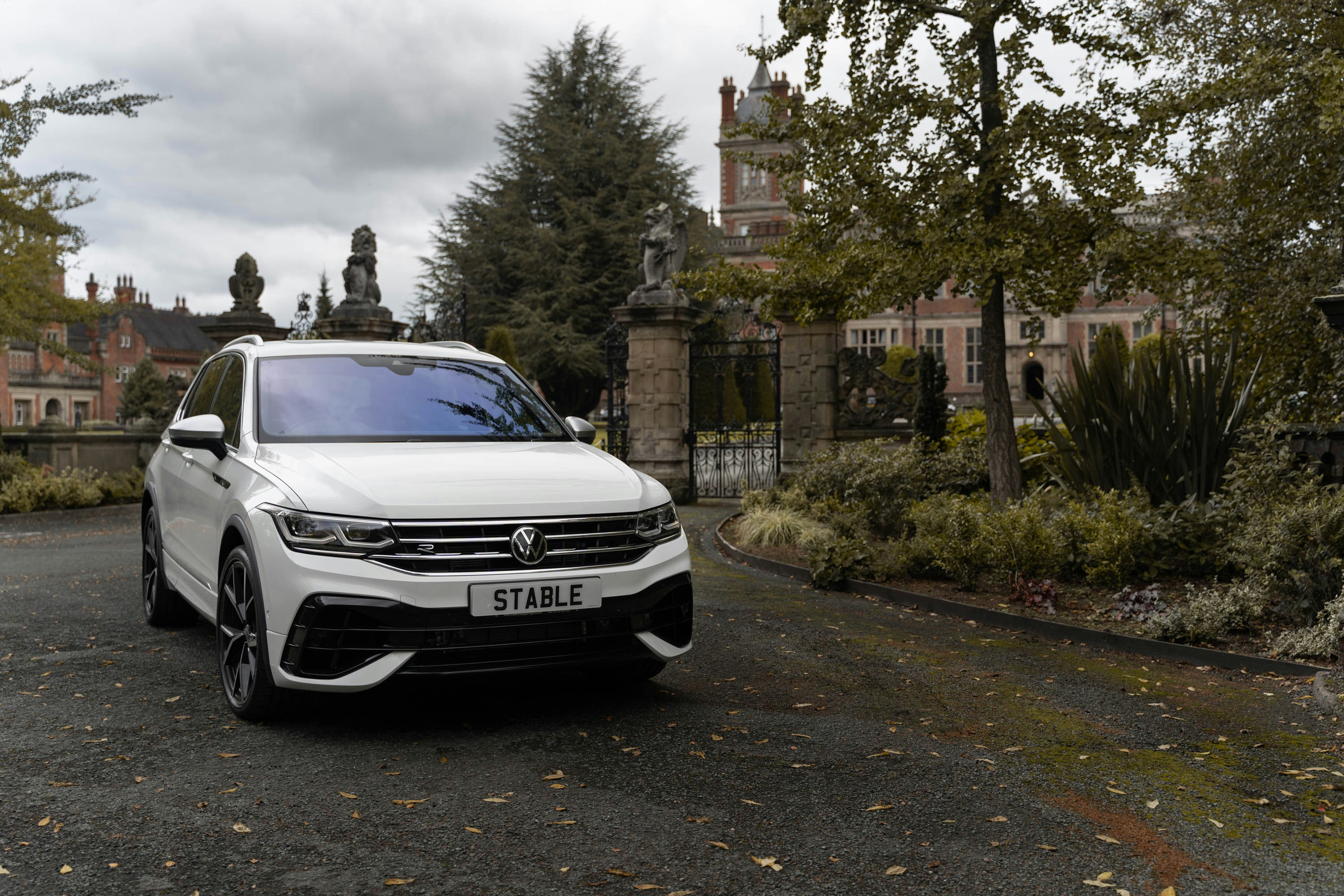 A sleek Volkswagen SUV parked on a rustic driveway, framed by lush greenery and an elegant estate in the background.