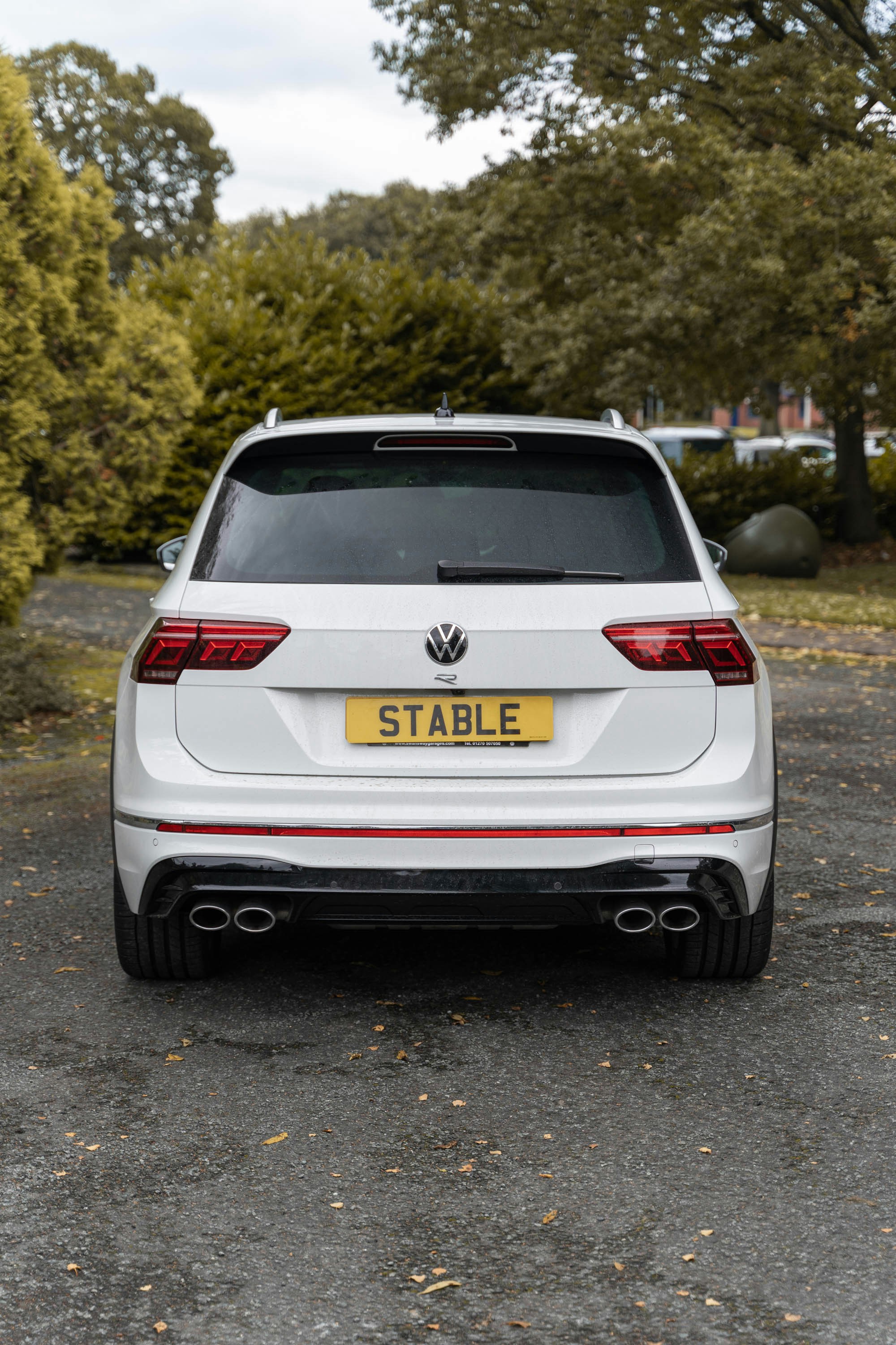 White Volkswagen SUV parked on a gravel path surrounded by lush greenery, showcasing its rear design and distinctive license plate.