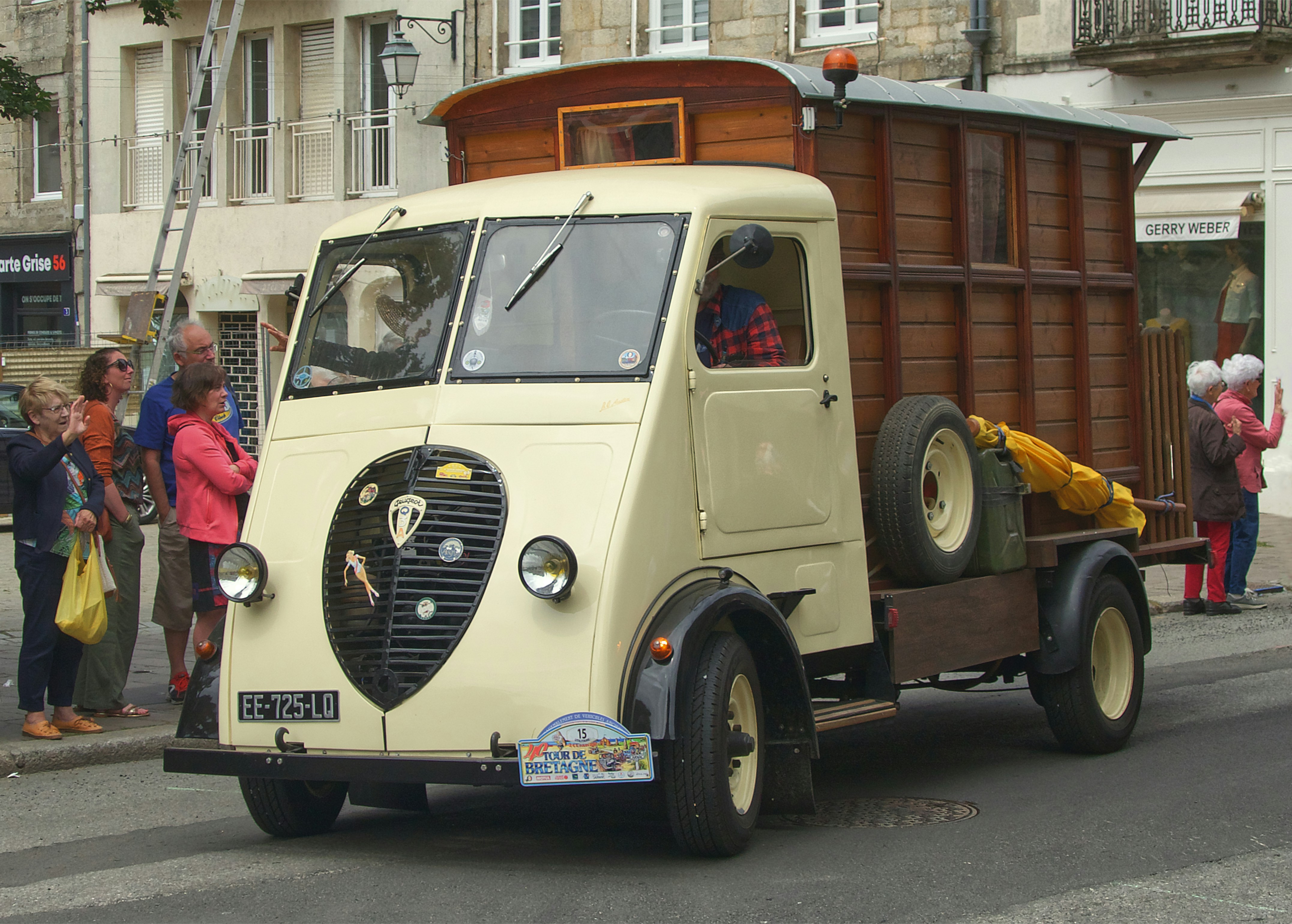 Classic vintage truck with wooden accents parked on a bustling street, surrounded by onlookers enjoying the scene.