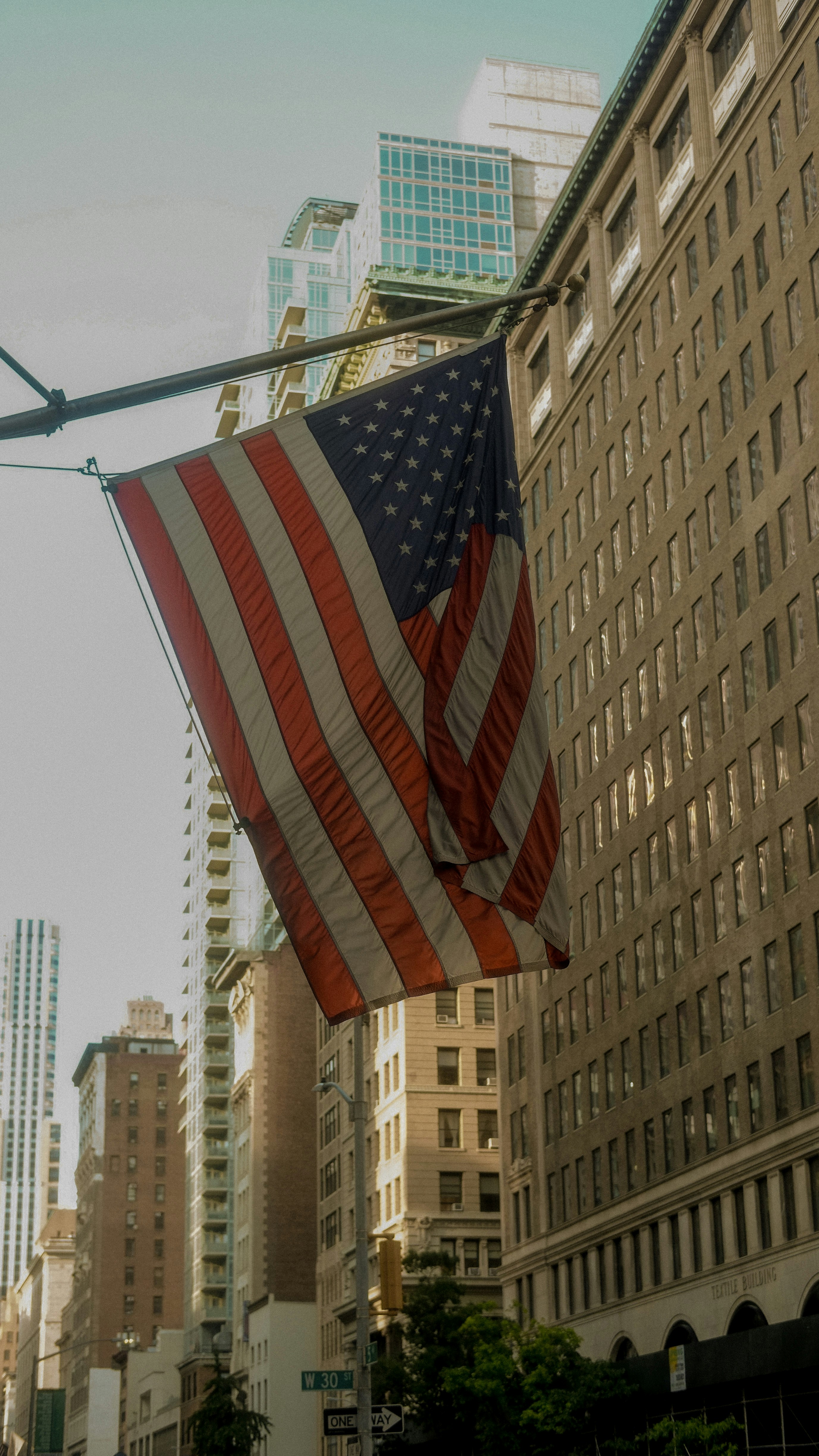 Flaglight Above Downtown: American Banner Between Brick and Glass