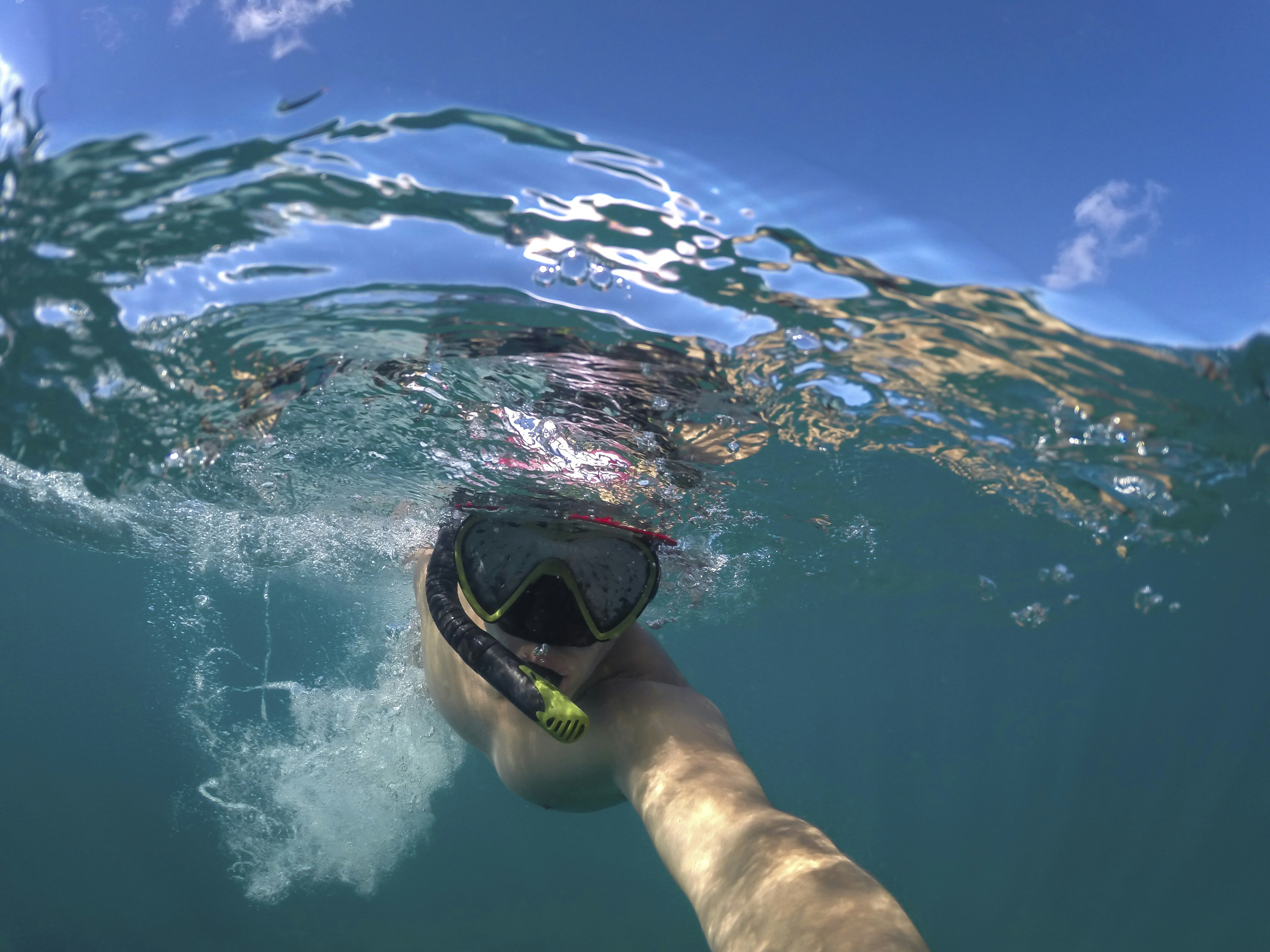 Snorkeler glides toward the camera underwater, mask and snorkel clearly visible as sunlight dances through the turquoise water.