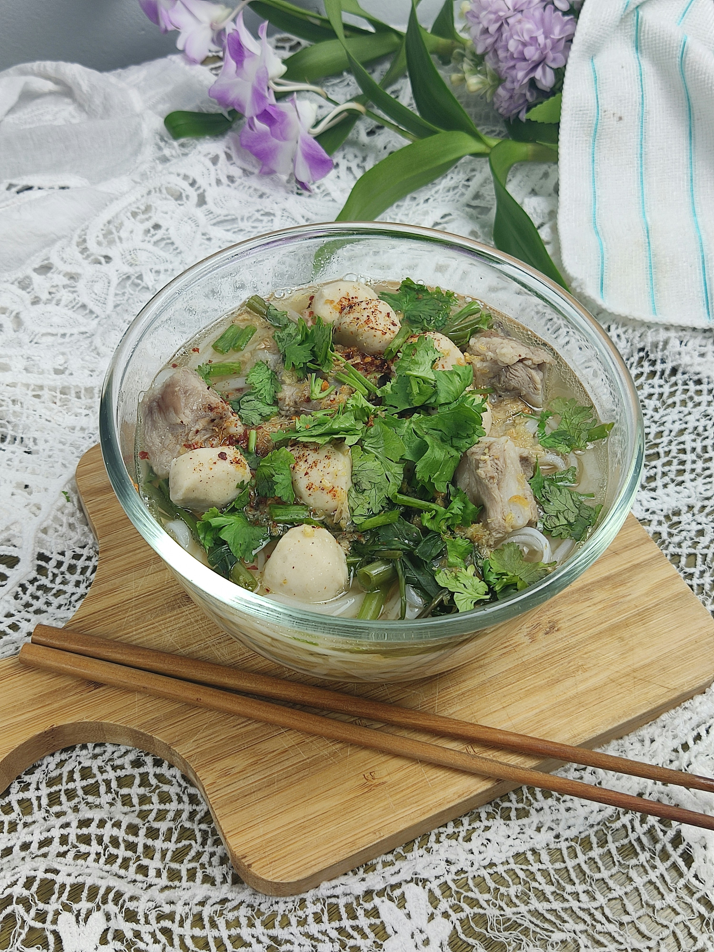 Delicious bowl of soup featuring meat and herbs, garnished with fresh cilantro, served on a wooden board with chopsticks. 