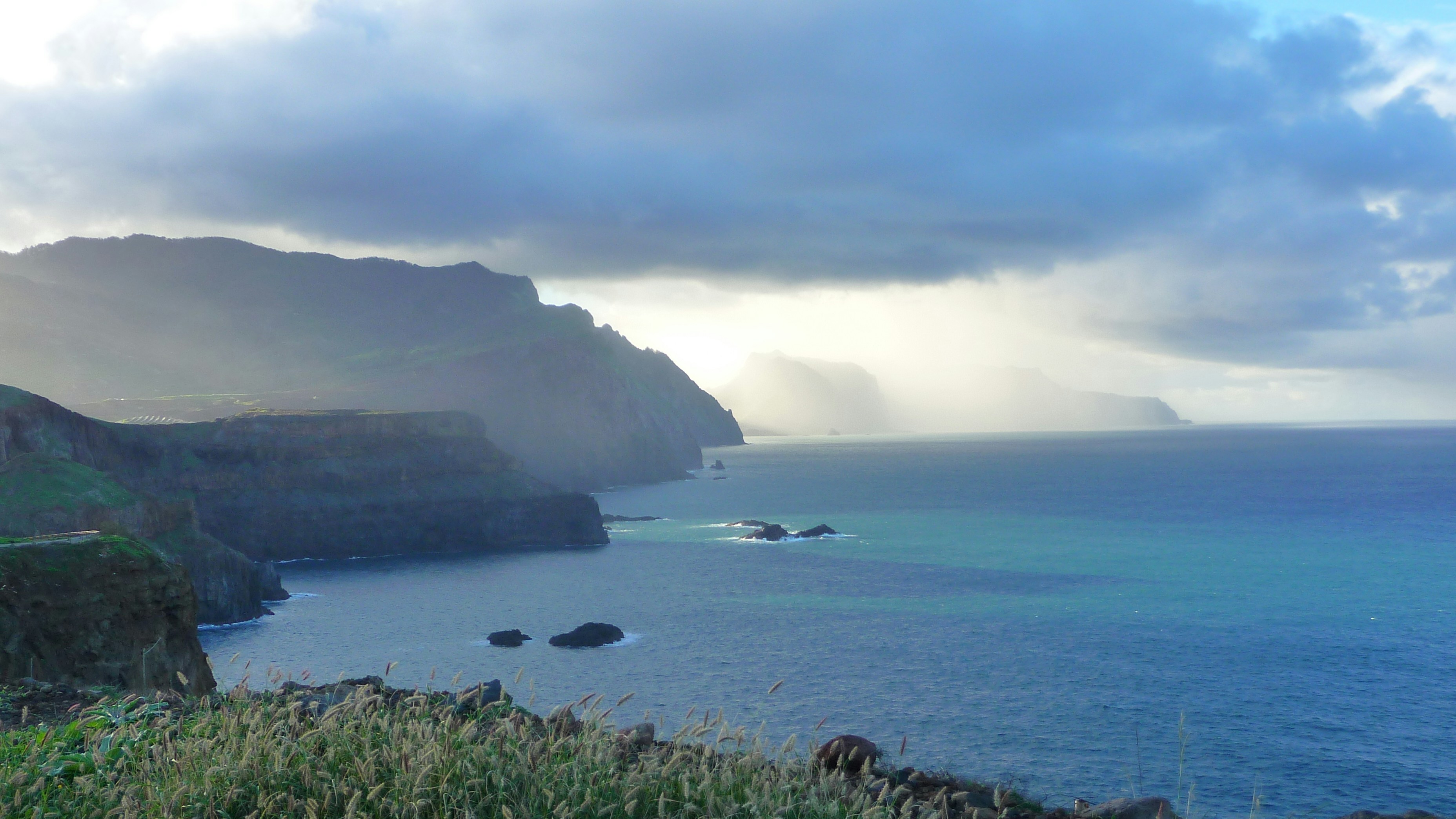 a body of water with hills and a beach with a hill and a cloudy sky