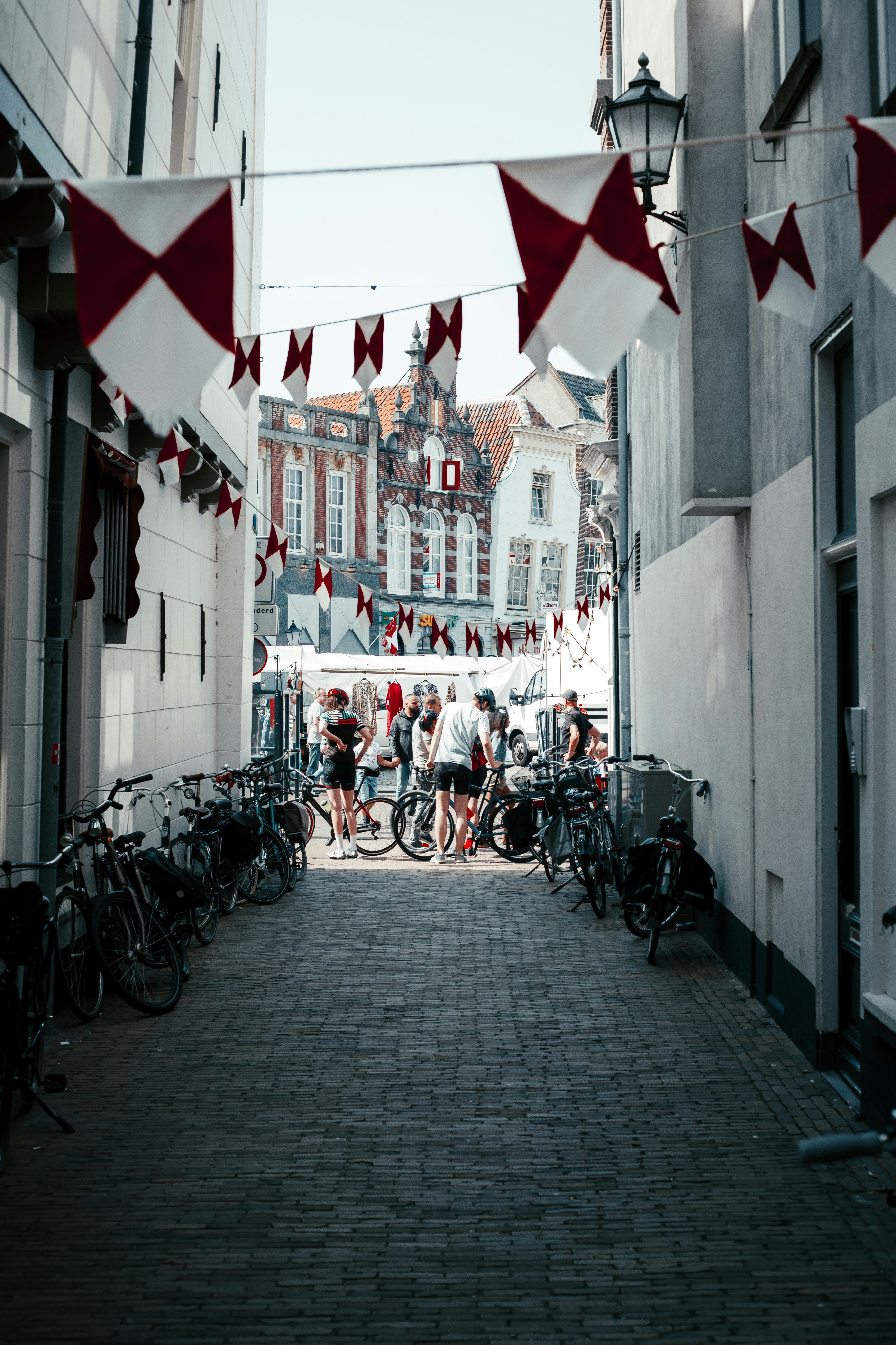 Pennant-Lined Alley: Cyclists and Friends Gather in a Sunlit European Backstreet