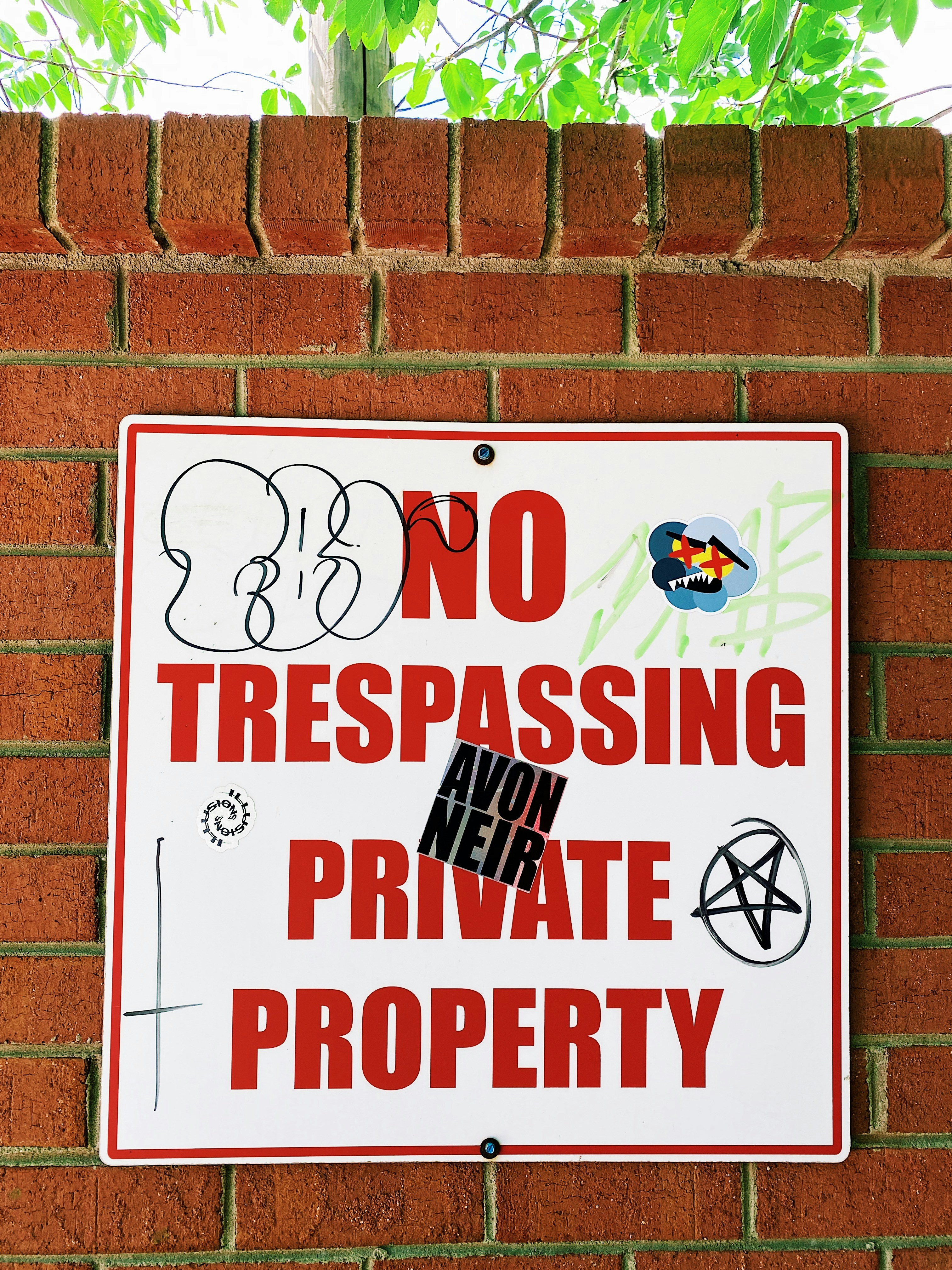 No Trespassing on Brick: Graffiti-Stamped Sign in Red and White
