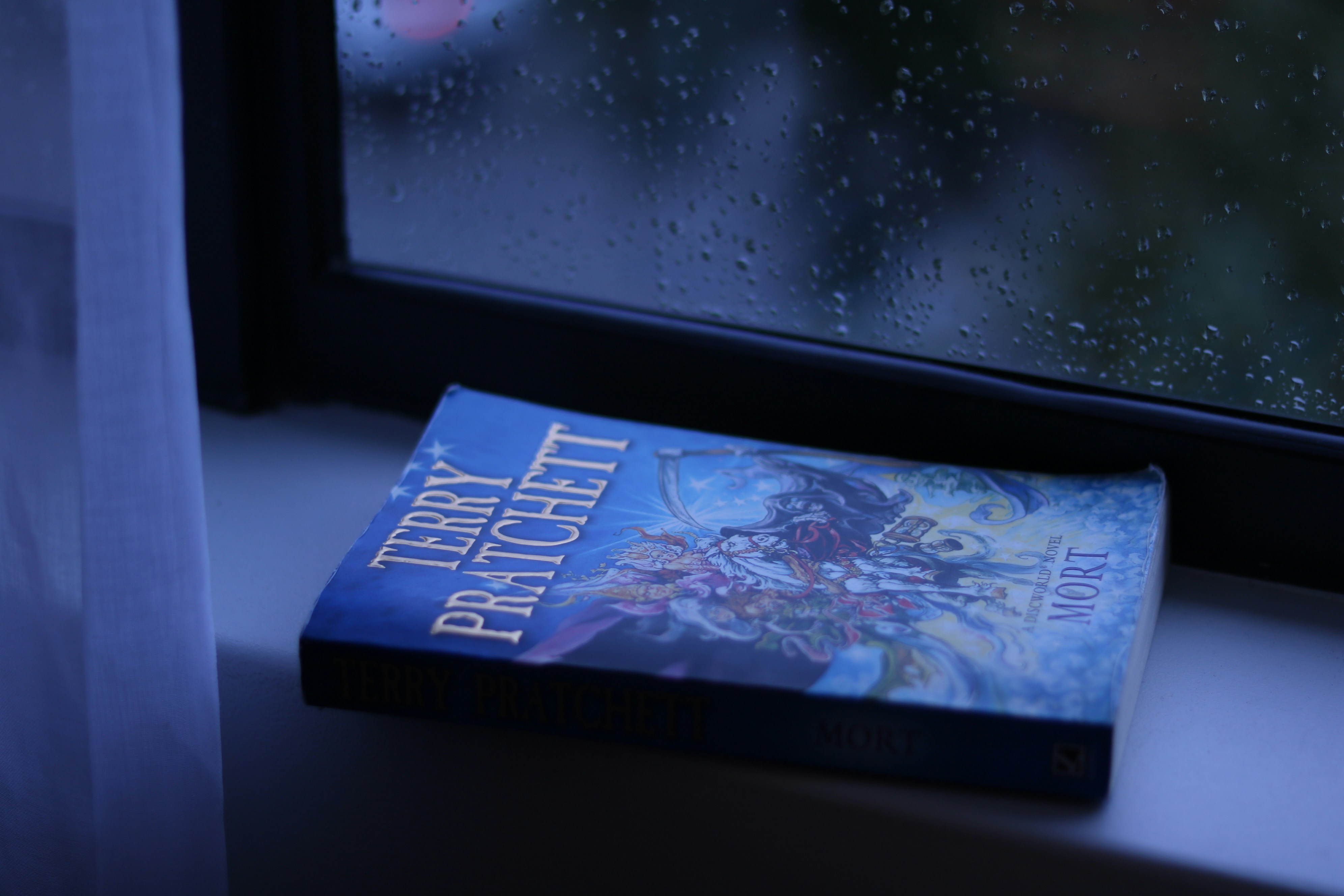 Book titled 'Mort' by a window with raindrops on the glass.
