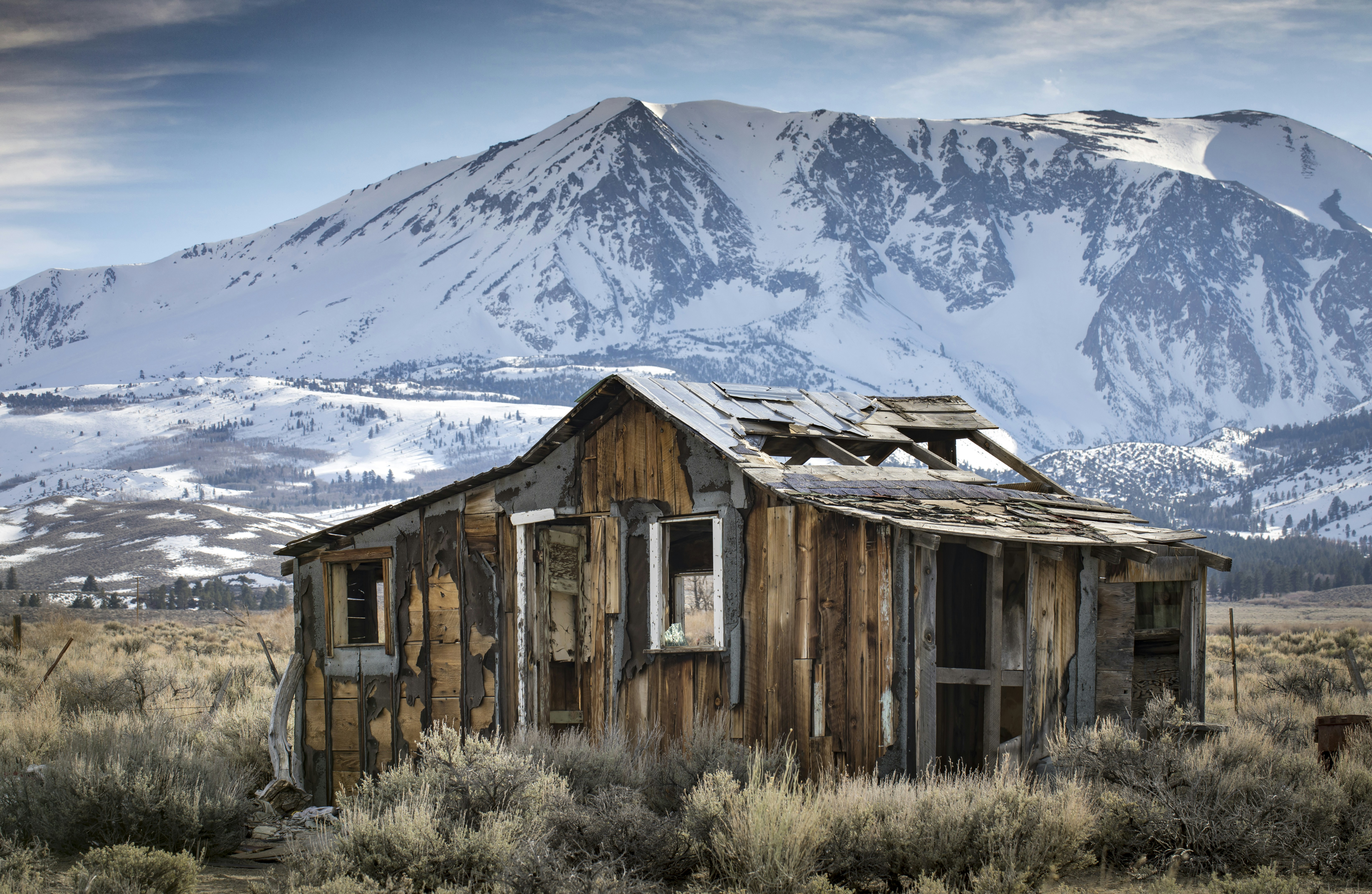 A wooden house in the middle of a field with snowy mountains in the ...