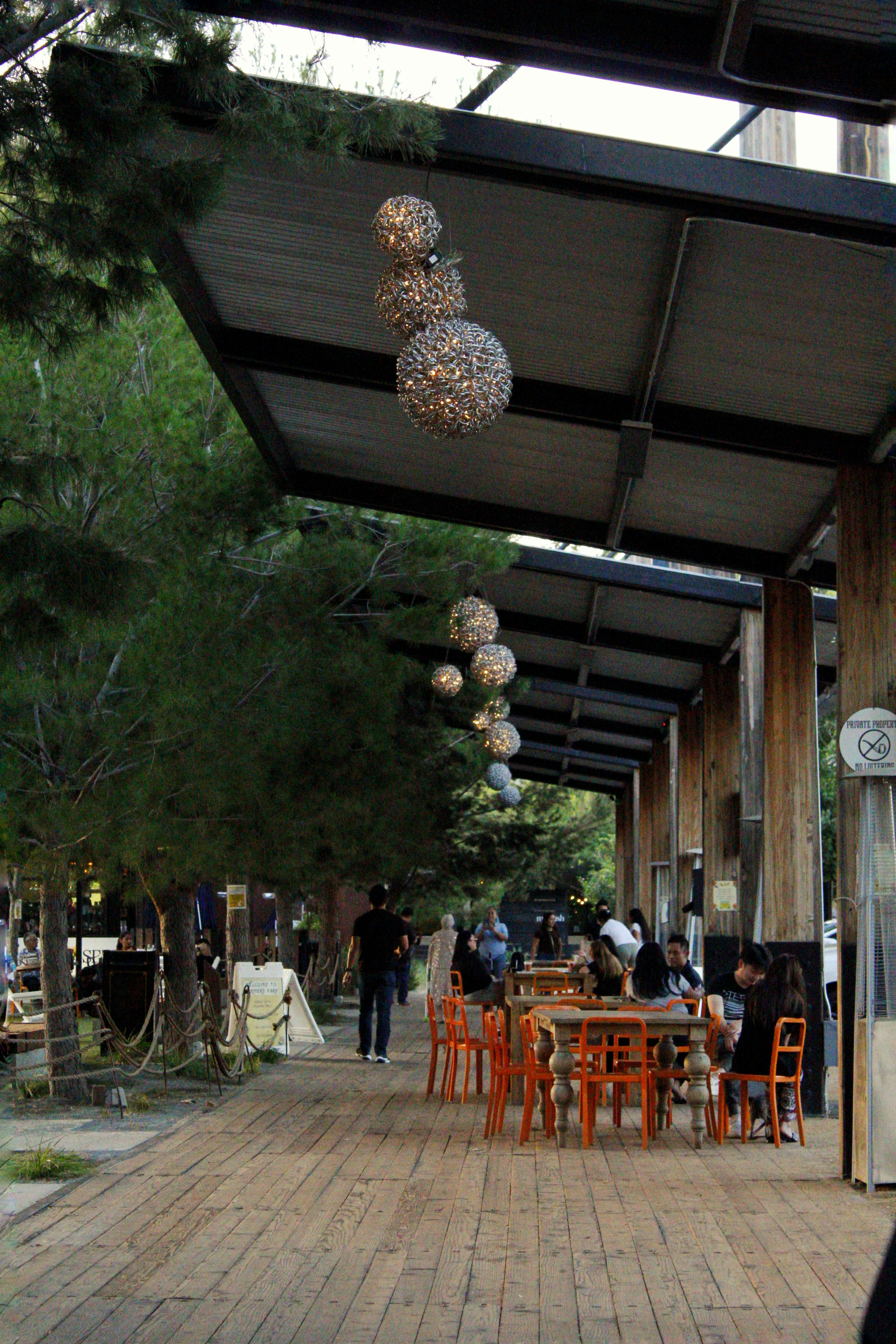A vibrant outdoor dining area featuring rustic wooden tables and hanging decorative lights amidst lush greenery.