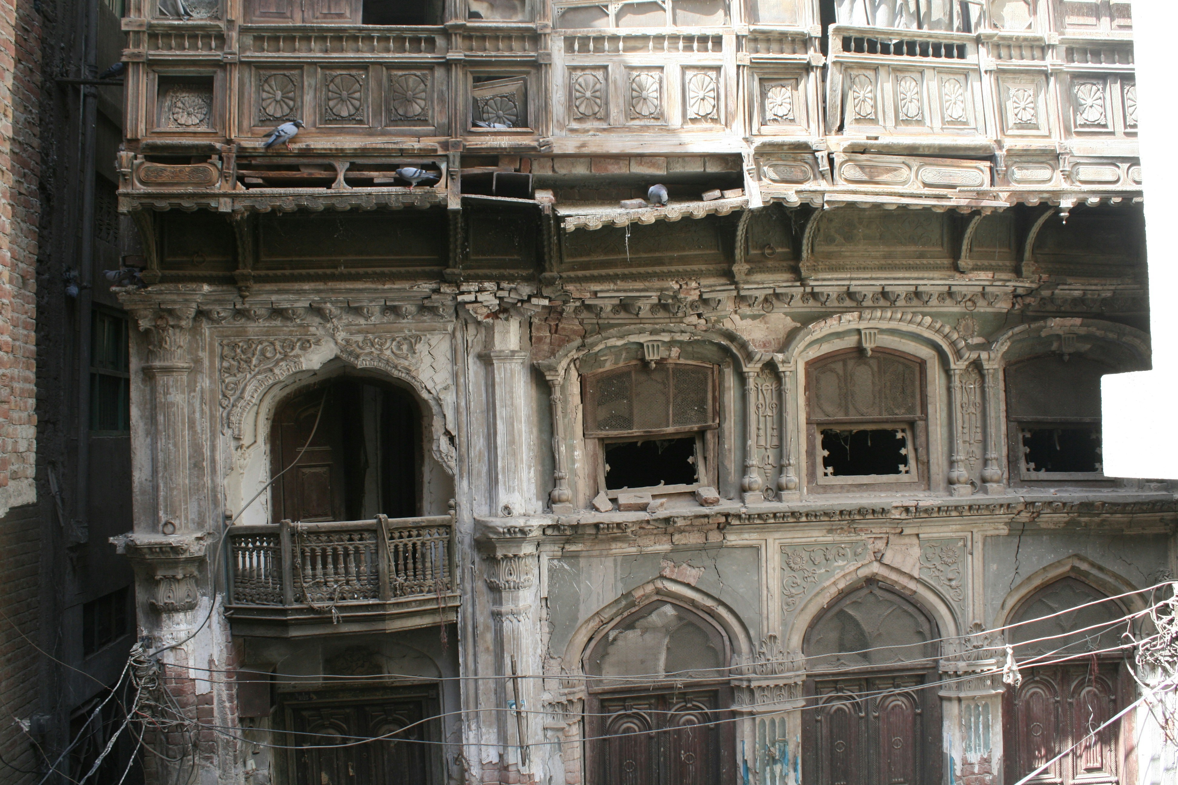 Dilapidated heritage building showcasing intricate wooden architecture, with broken windows and peeling paint. The remnants of its grandeur tell a story of time gone by.