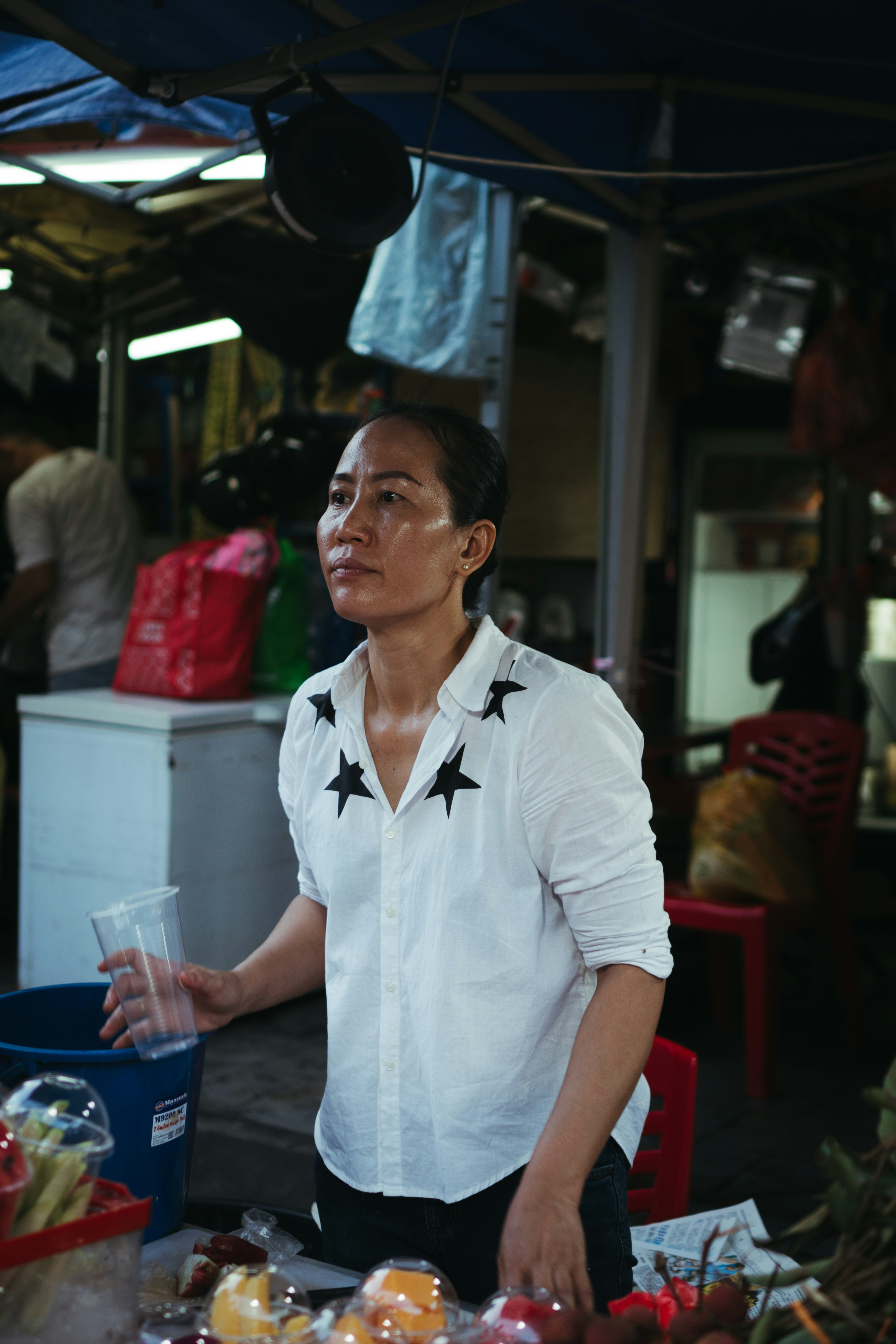 Market Vendor Under Blue Canopy: Focused Portrait at a Bustling Stall