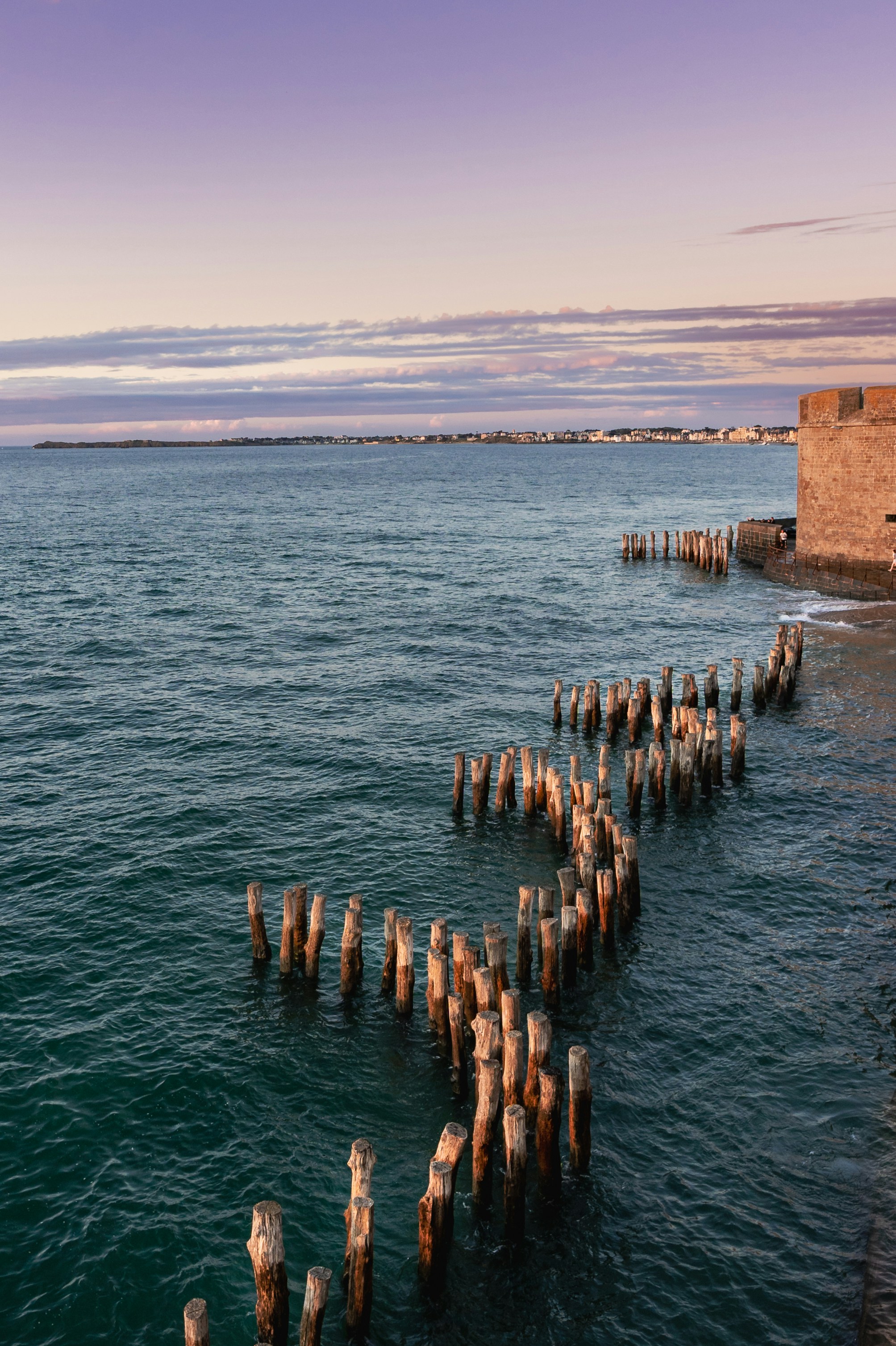 Arc of Pylons: Timber Posts Guiding the Sea Toward a Sunset Fortress