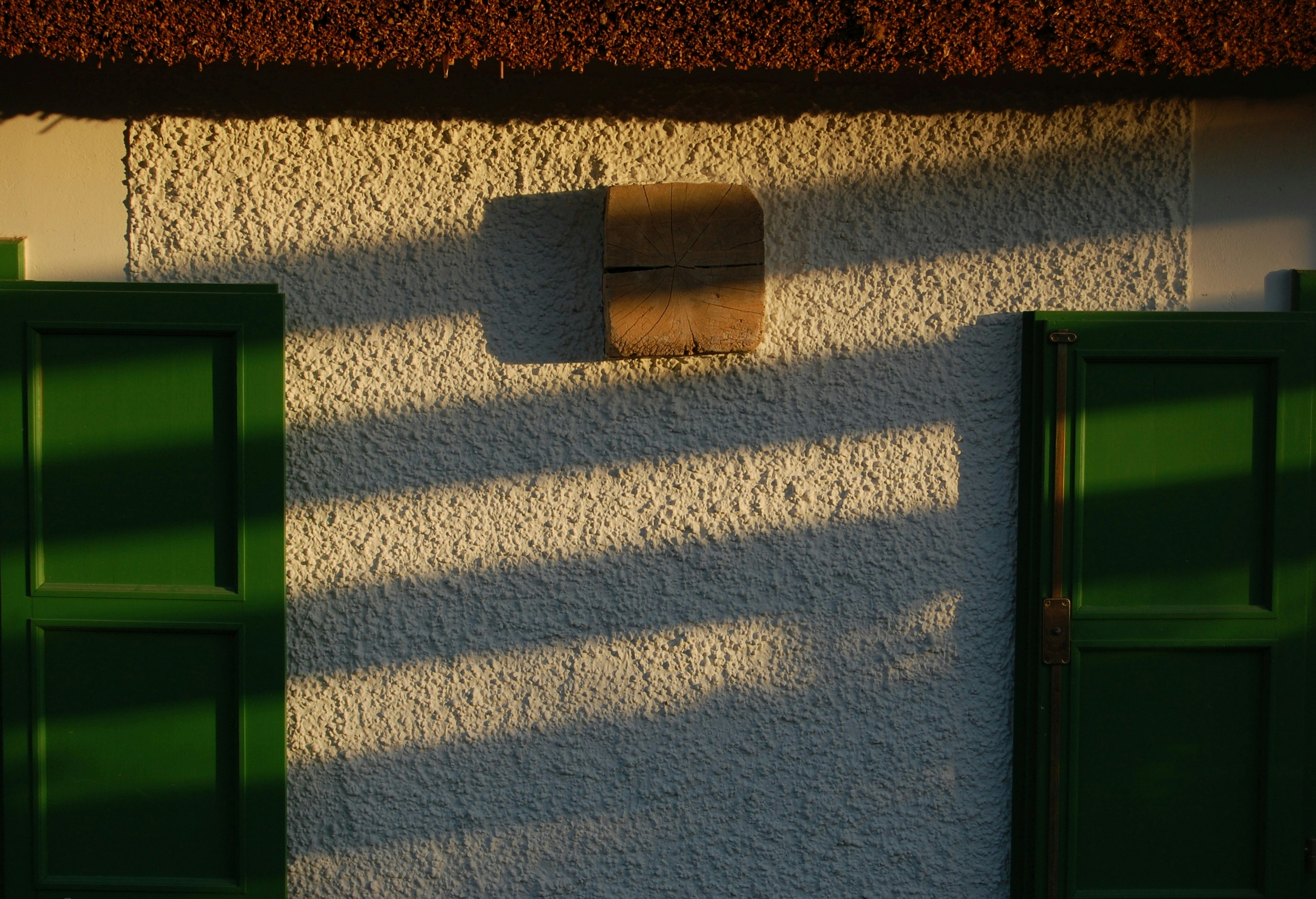 Golden Stripes on a Green Facade: Shadow Play Across Stucco