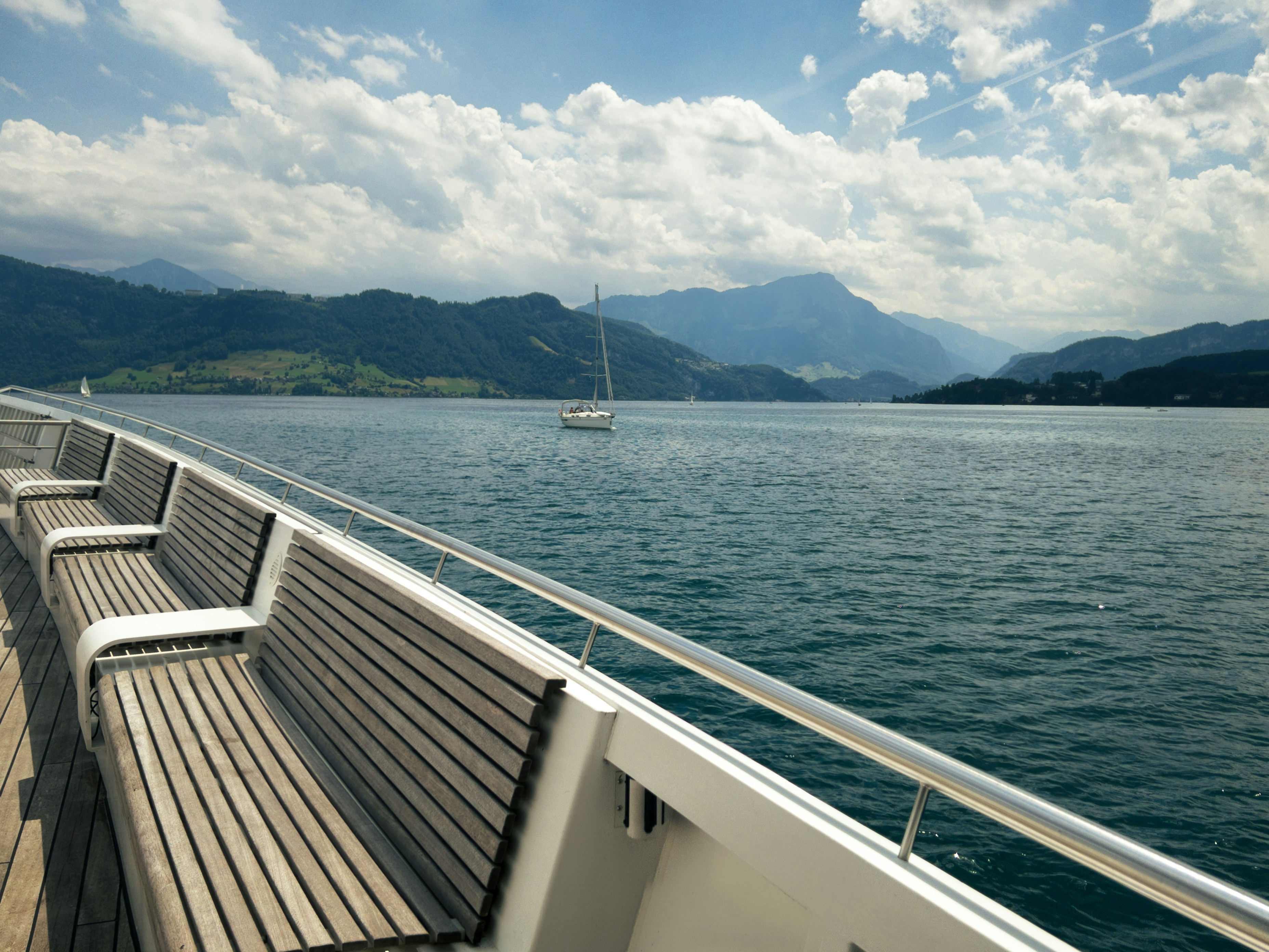 Lakeside Promenade Toward a Sailboat Beneath Alpine Peaks