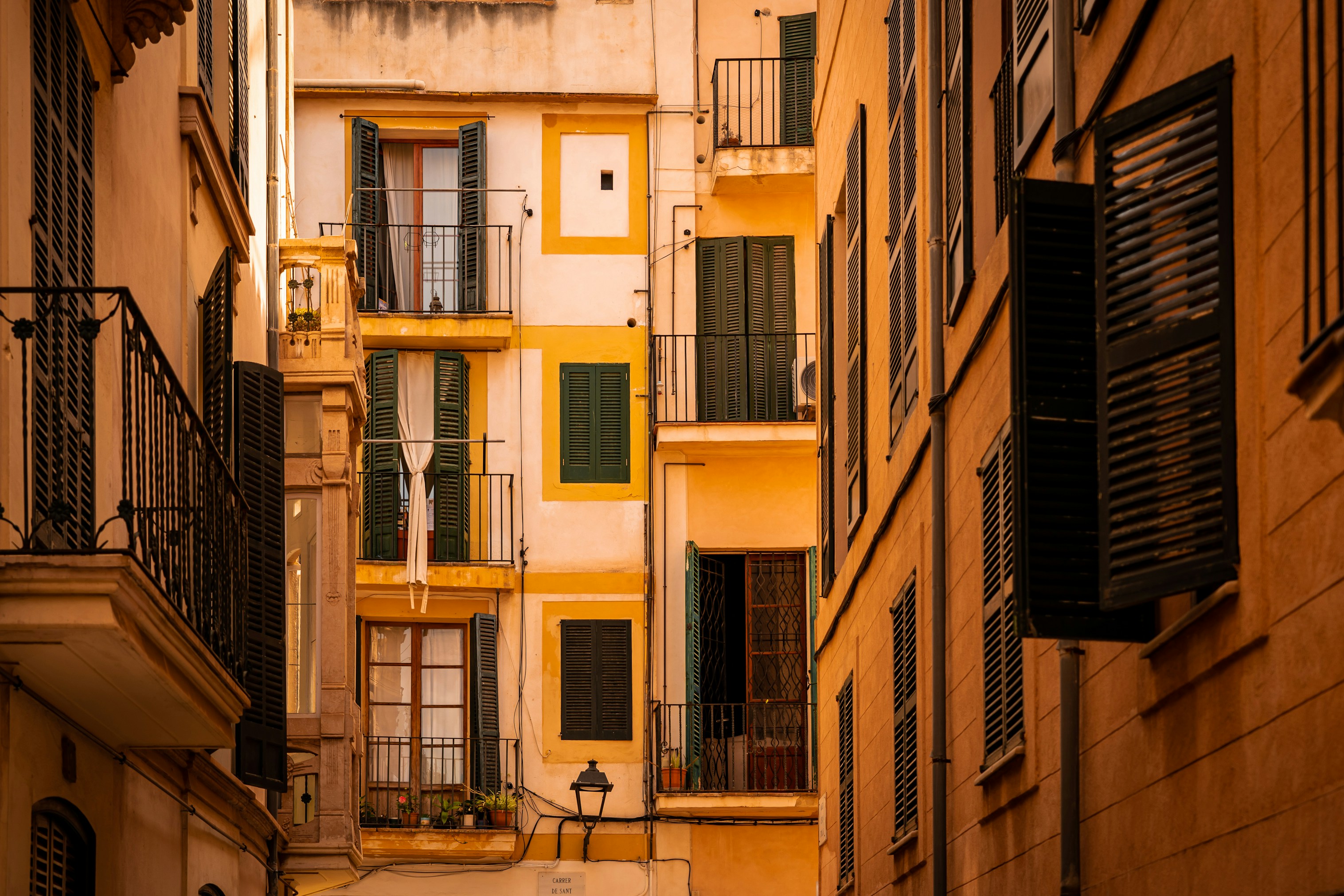 Warm-toned buildings with shuttered windows and wrought iron balconies lining a narrow street.