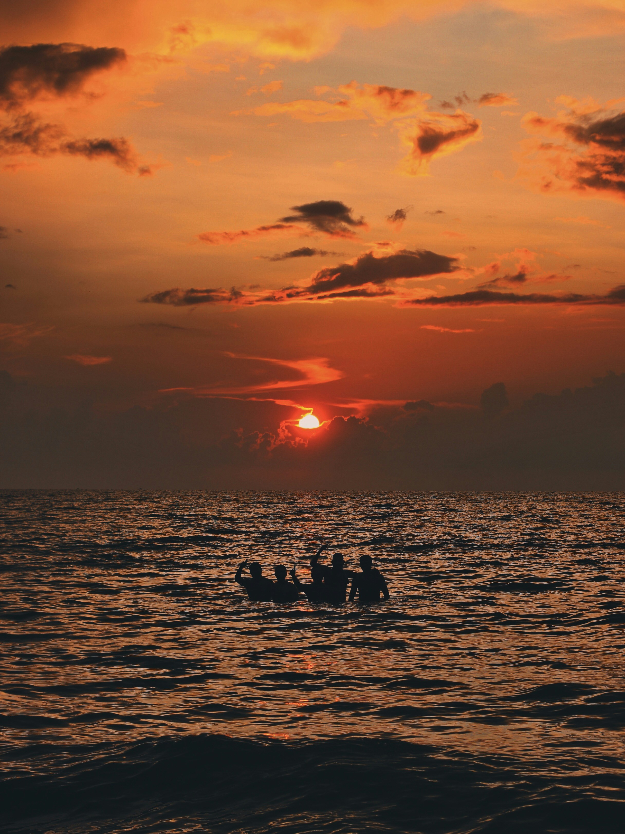 Fiery Horizon Silhouettes: A Tiny Crew Embracing Sunset on a Calm Sea