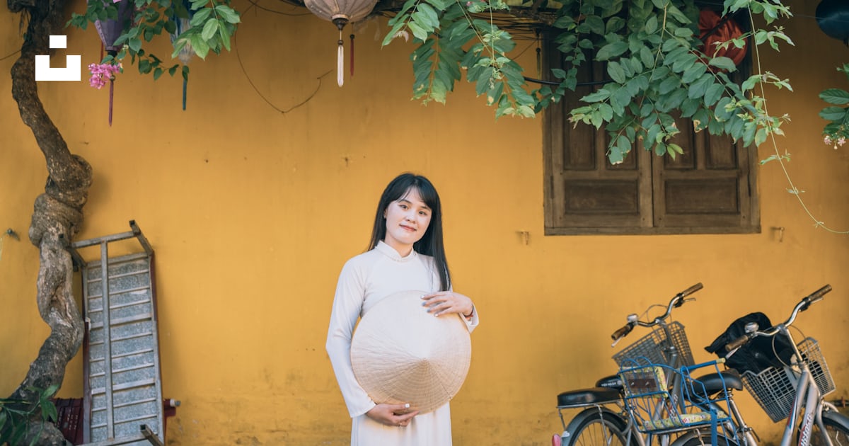 하얀 드레스를 입은 사람이 나무와 꽃이 있는 건물 앞에 서 있다 사진 Unsplash의 무료 기계 이미지