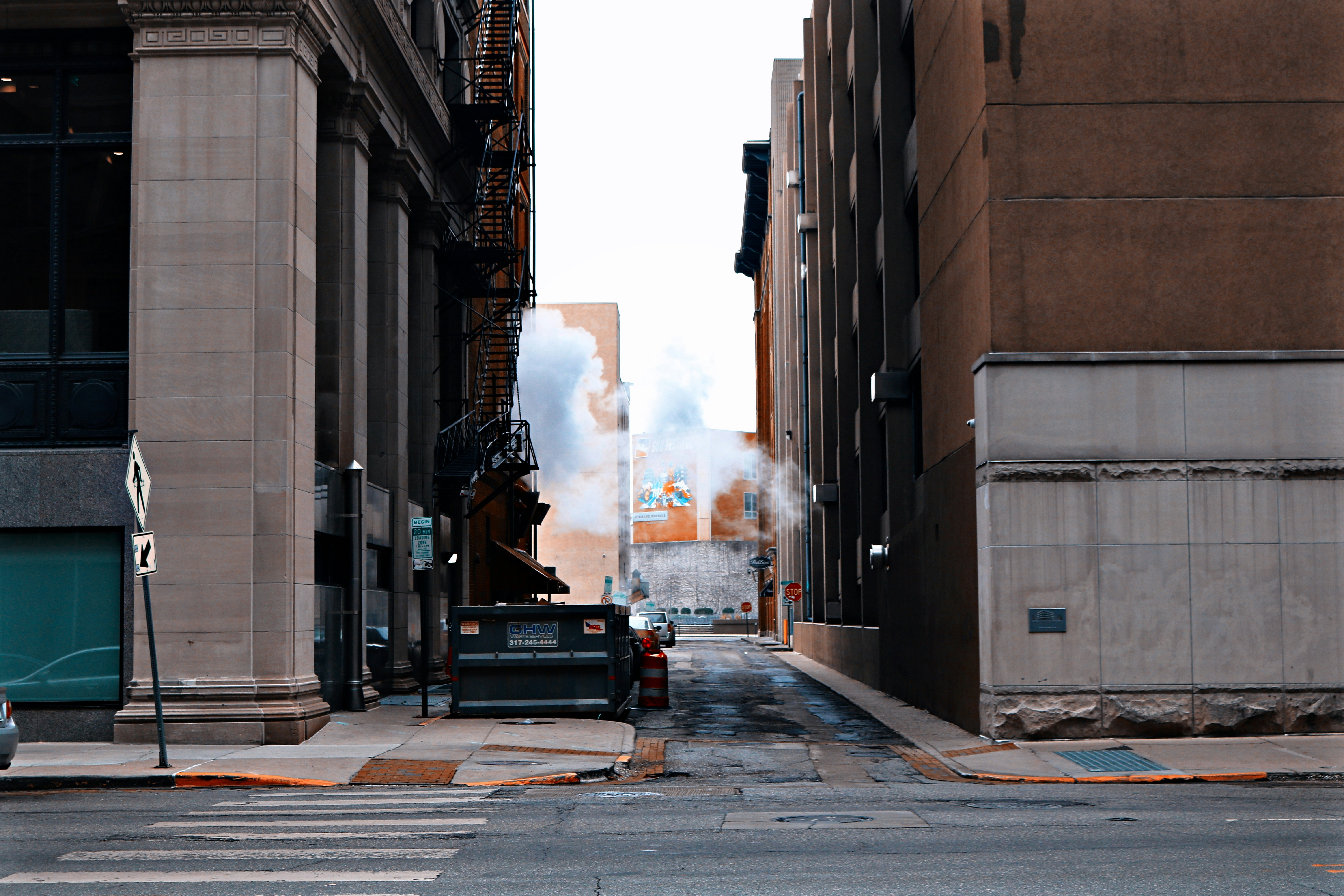 Steam billows between tall buildings along a quiet city alley.