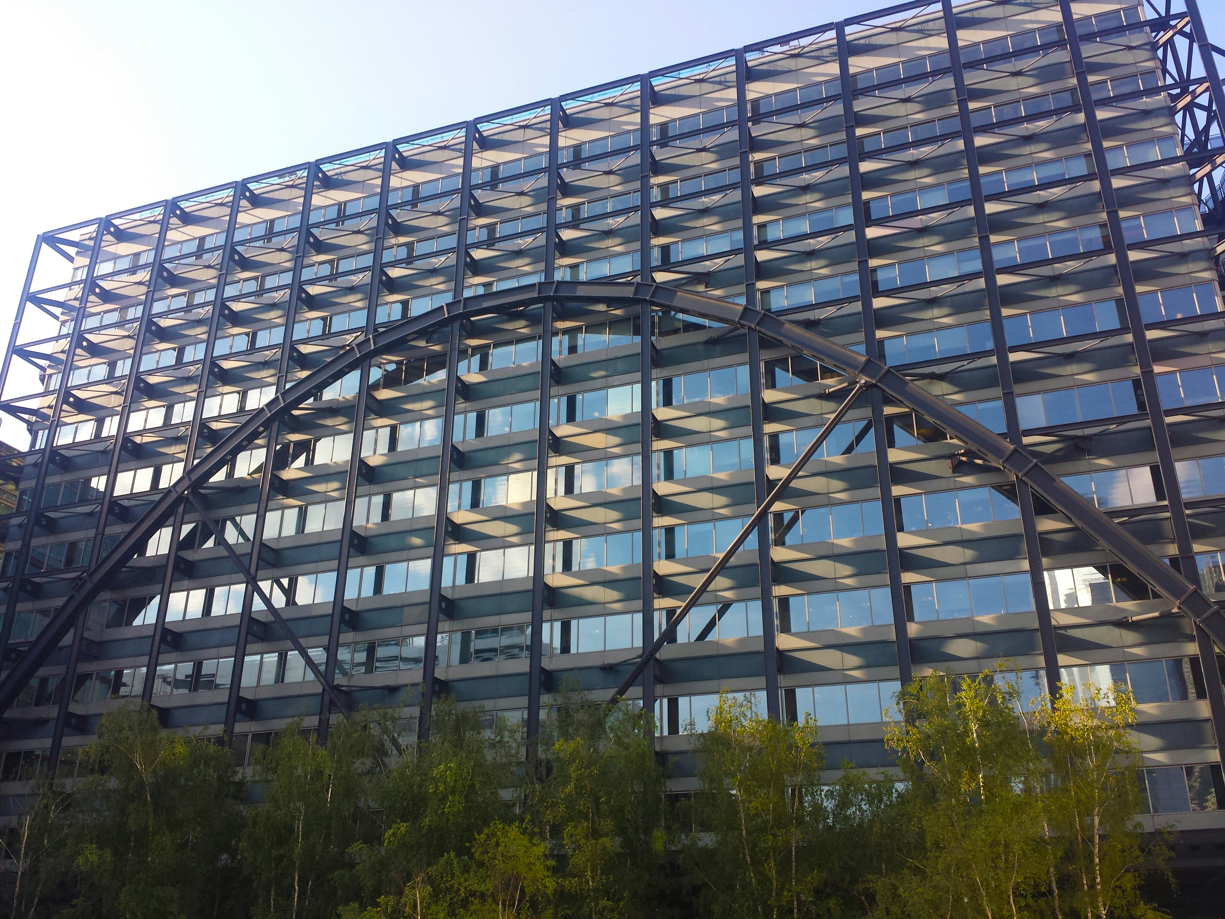 Modern office building featuring a striking steel arch structure against a backdrop of reflective glass windows and greenery.